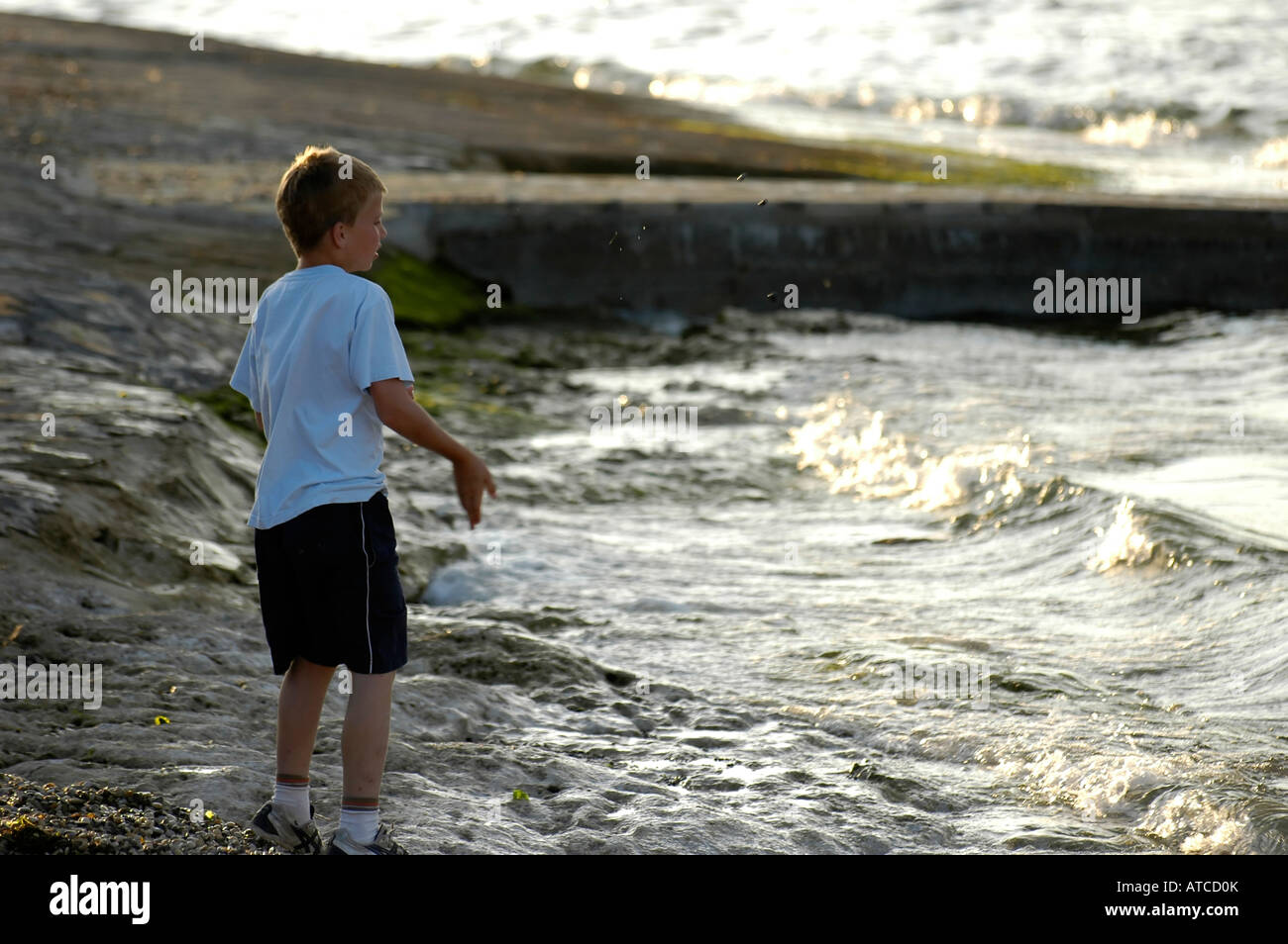Young boy throwing pebbles into the sea Stock Photo - Alamy
