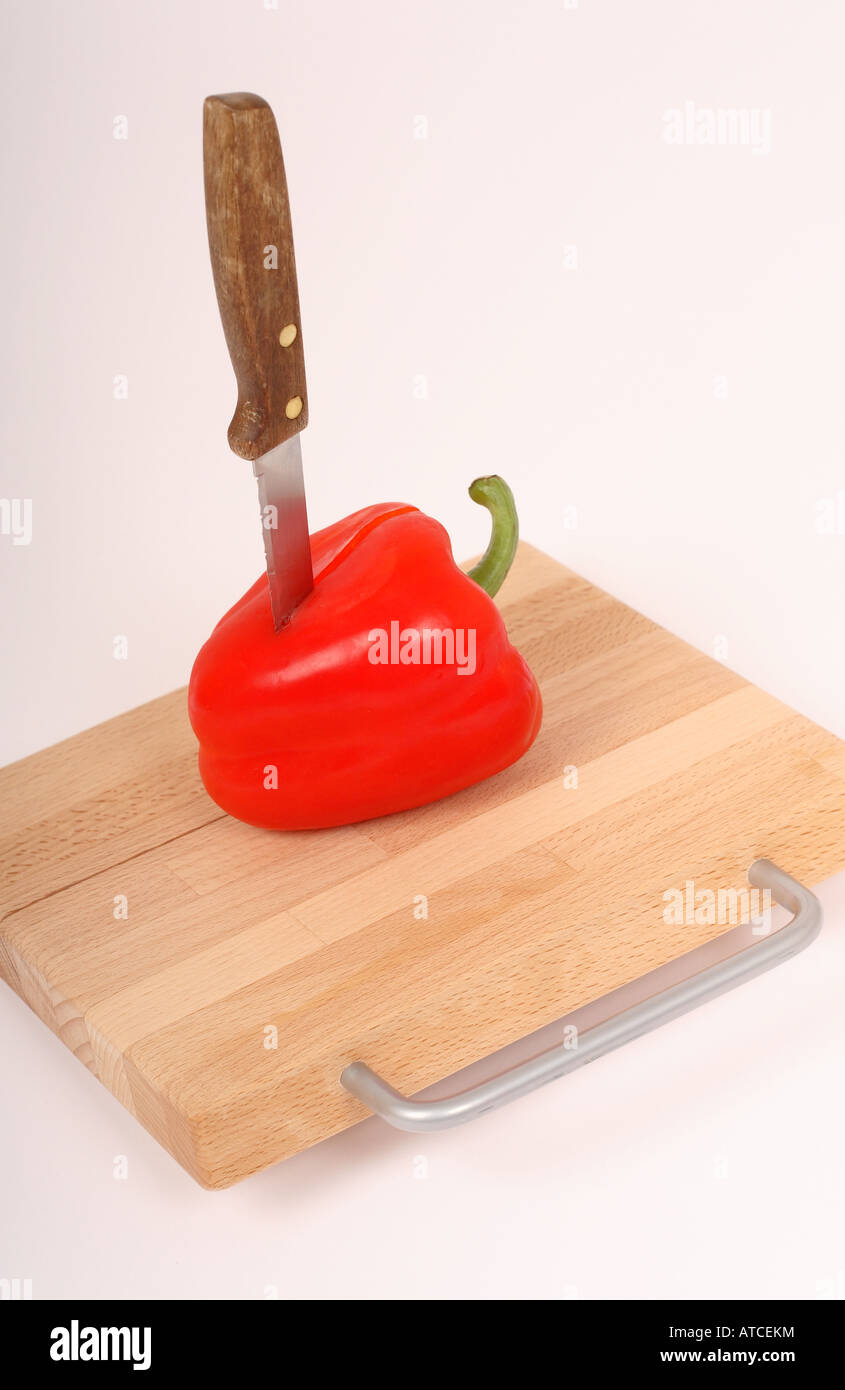 Red capsicum pepper on kitchen wooden chopping board with sharp knife ...
