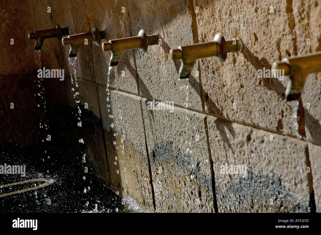 Five dripping taps along a stone wall Stock Photo - Alamy