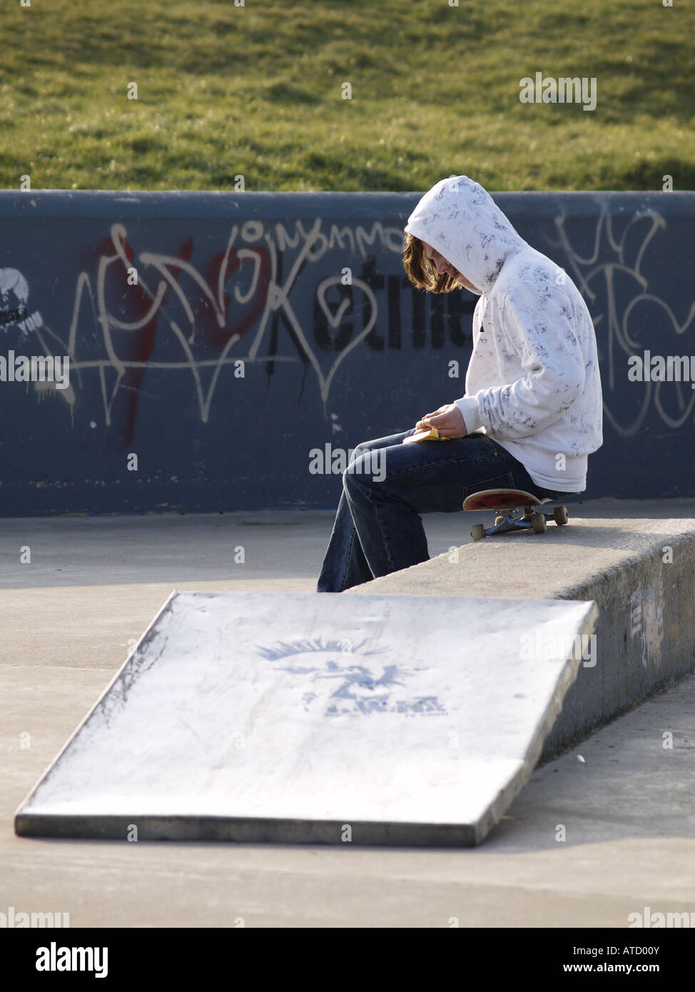 Teenage skateboarder, in skate park, sat on his skateboard, rolling a ...