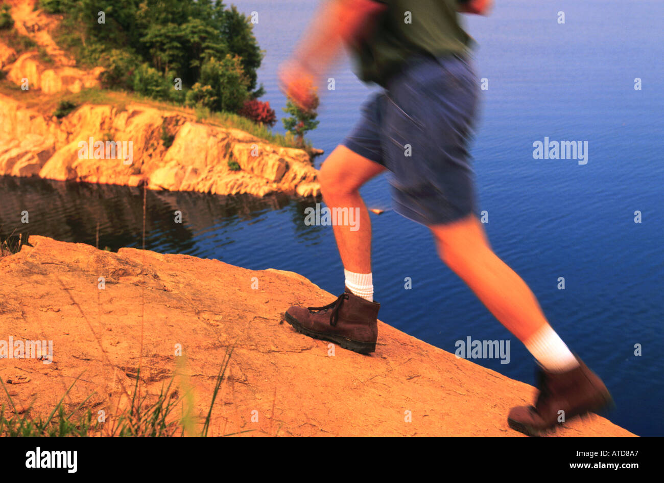 Close up of a hikers legs walking across a rocky ledge with a lake ...