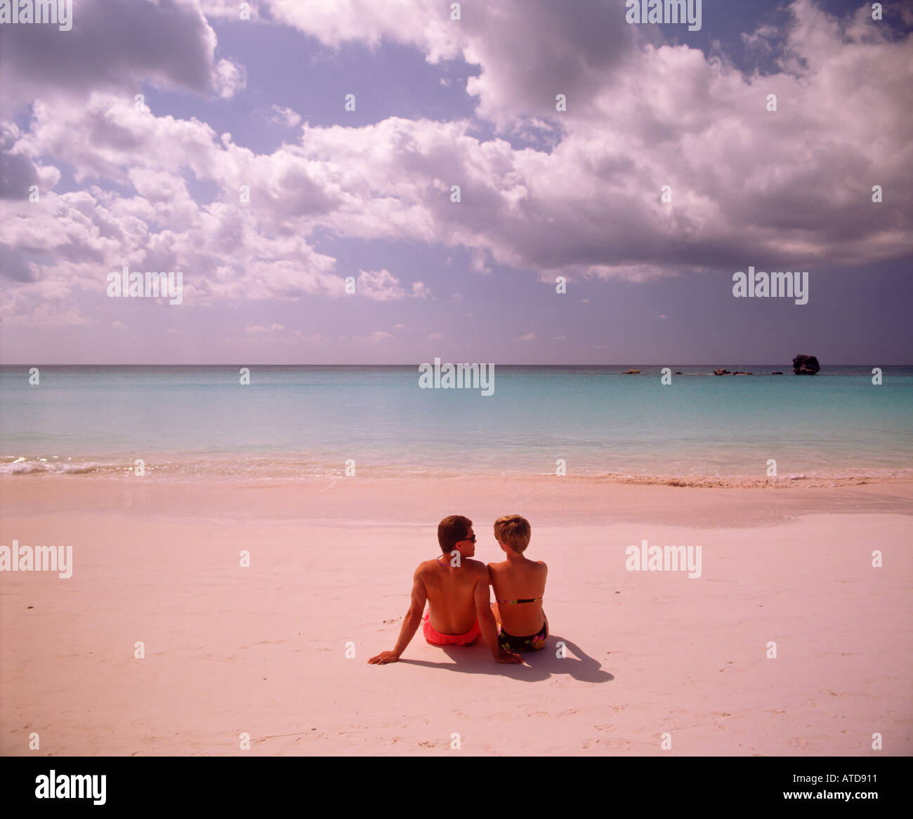 a-couple-sitting-side-by-side-in-the-pristine-pink-sand-of-horseshoe