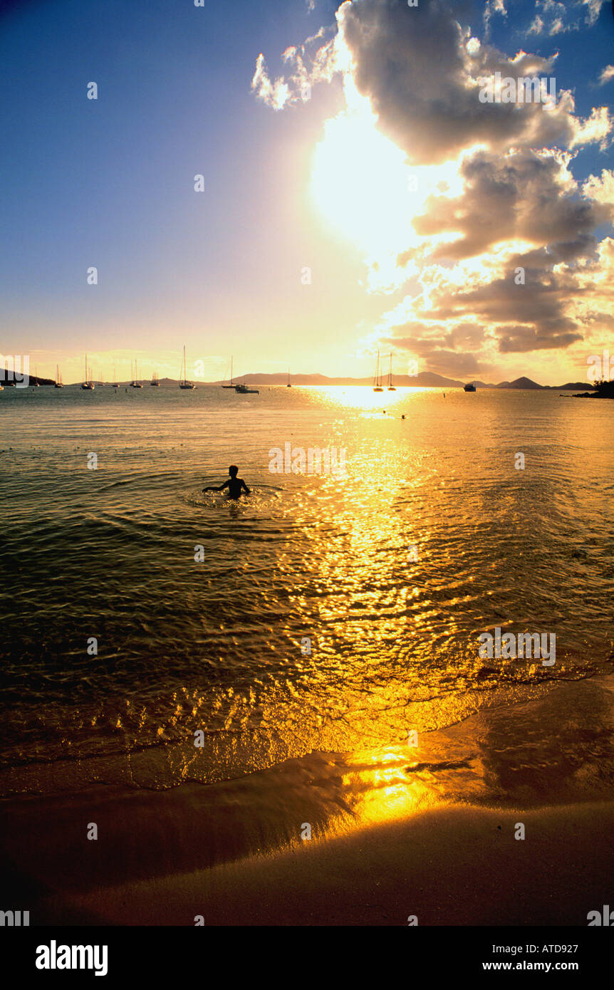 The sun reflects off of water as it sets behind clouds as a swimmer ...