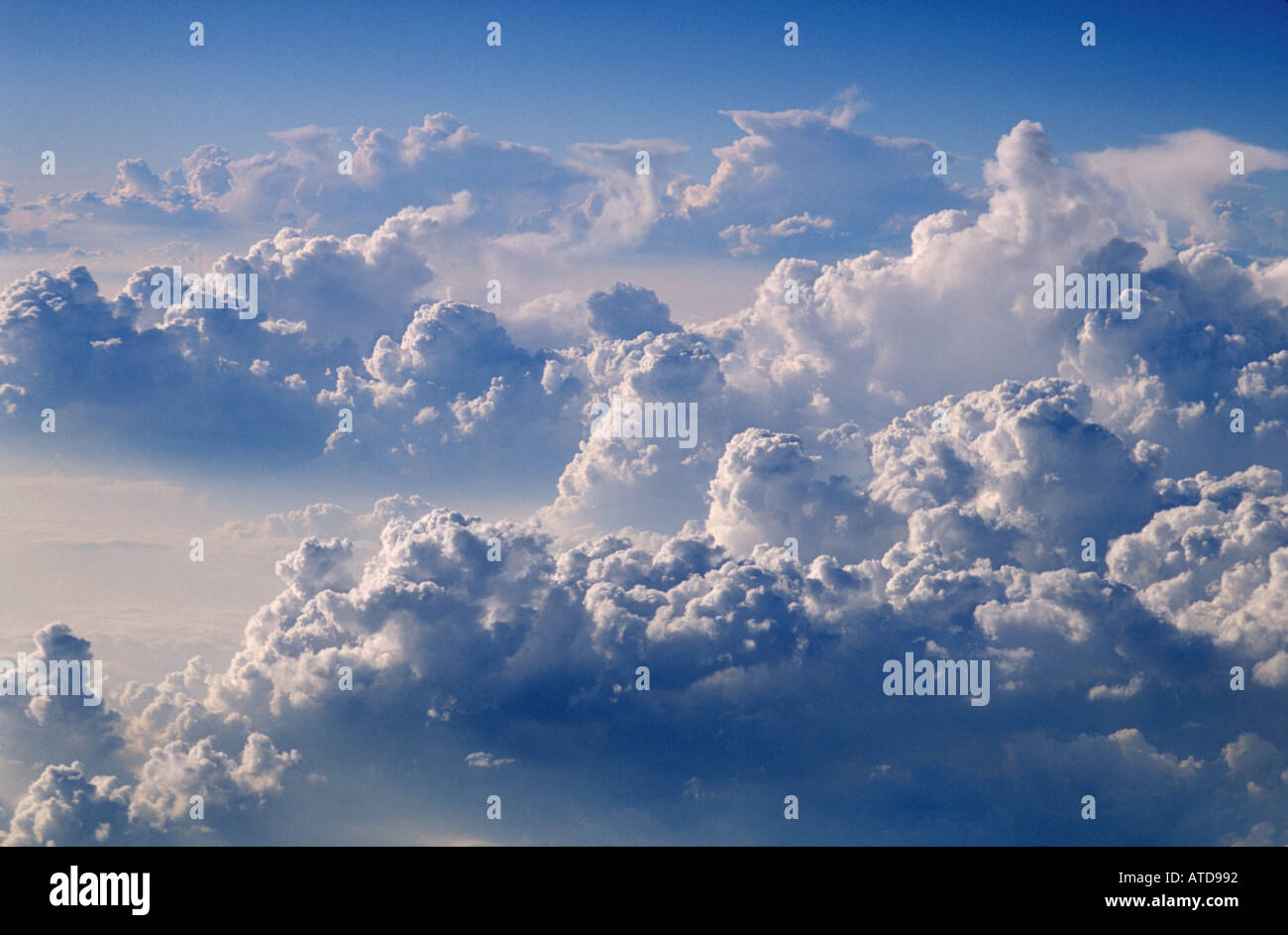 Billowy clouds fill a pale blue sky from above shot from an airplane ...