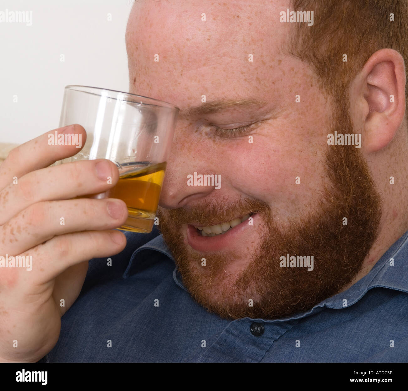 young man smiling holding a glass of whisky tenderly against his face ...