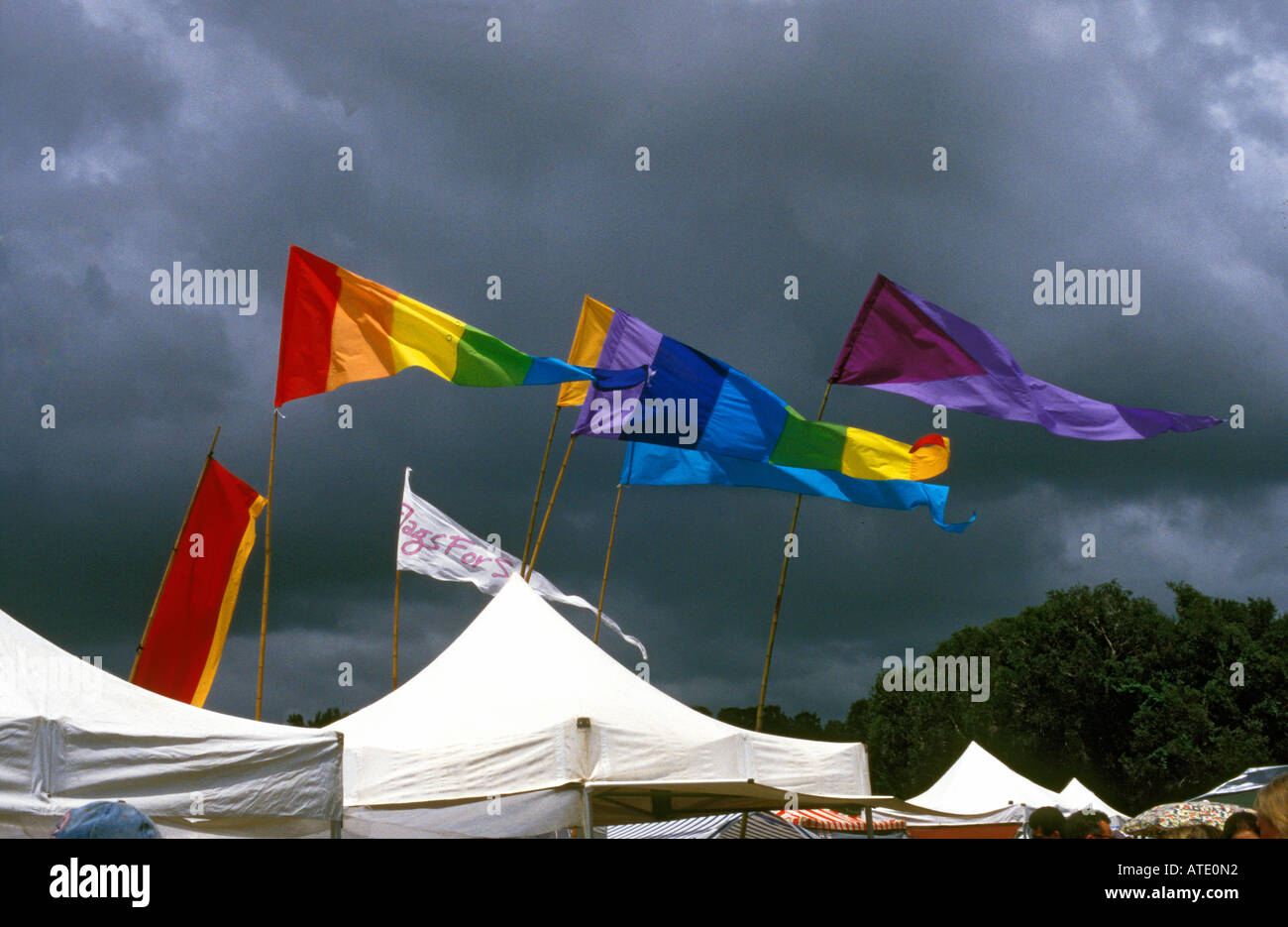 Colourful banners flying in a strong wind above white tents under dark ...
