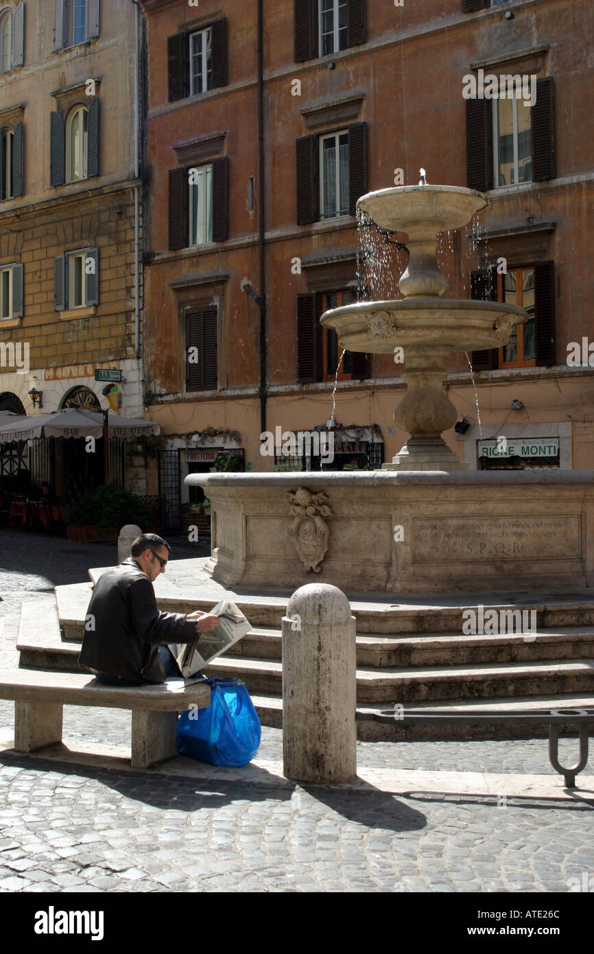 Man reading a newspaper by a fountain in a small square in Rome Italy ...