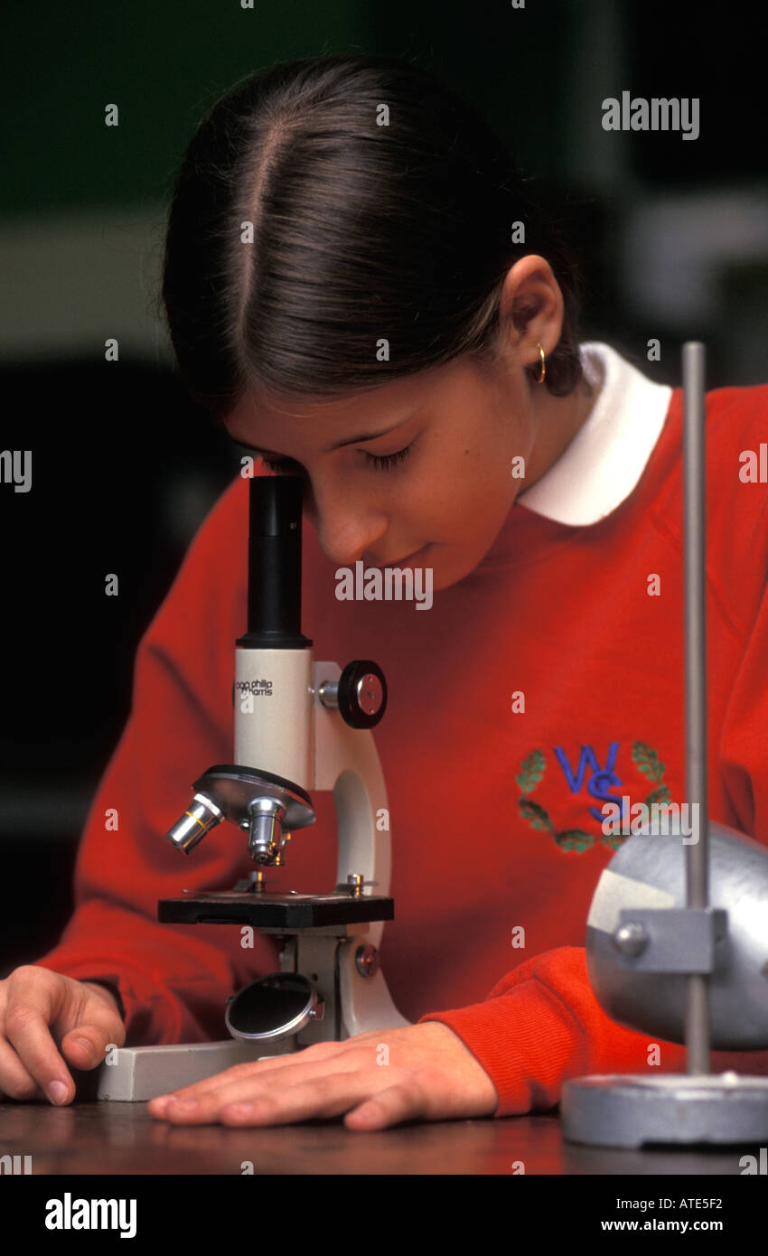 Secondary school girl looking through microscope in science class ...