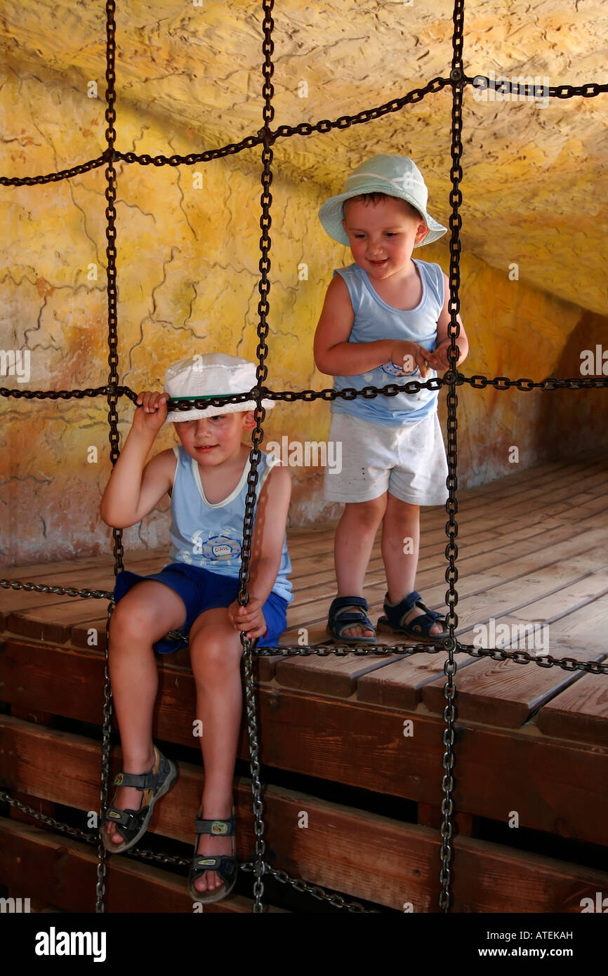 Young boys sitting on ledge near chain links, kids play in cave on ...