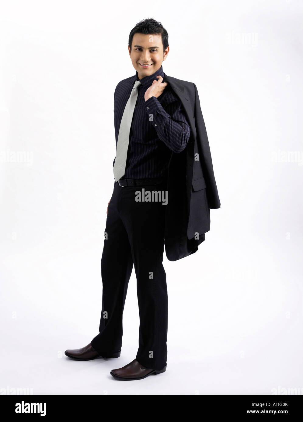 Smiling businessman holding suit jacket over shoulder posing in studio ...