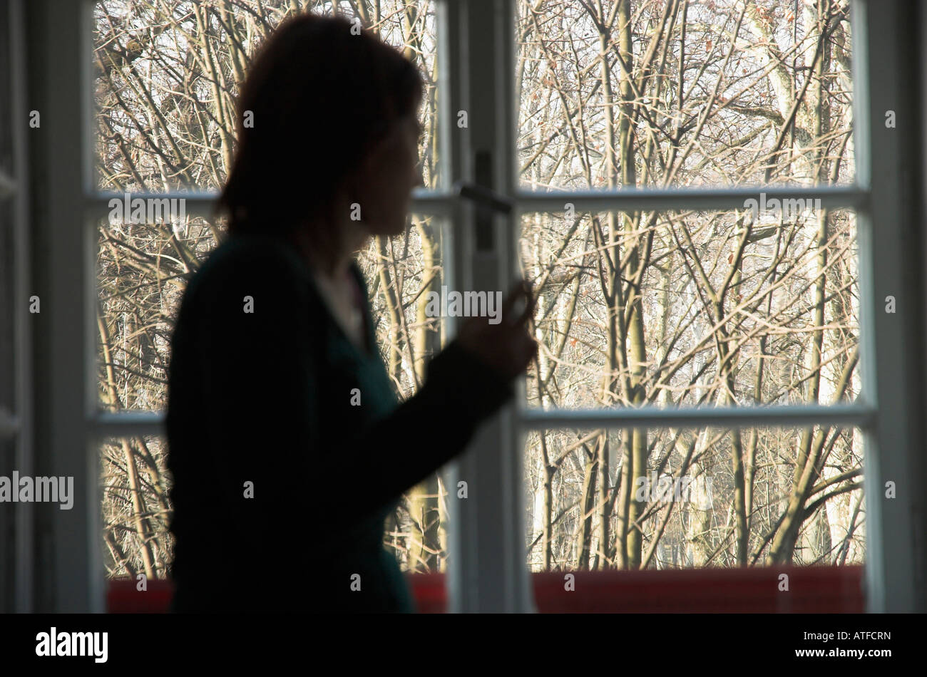 Woman silhouetted against window light looking out of window Stock ...
