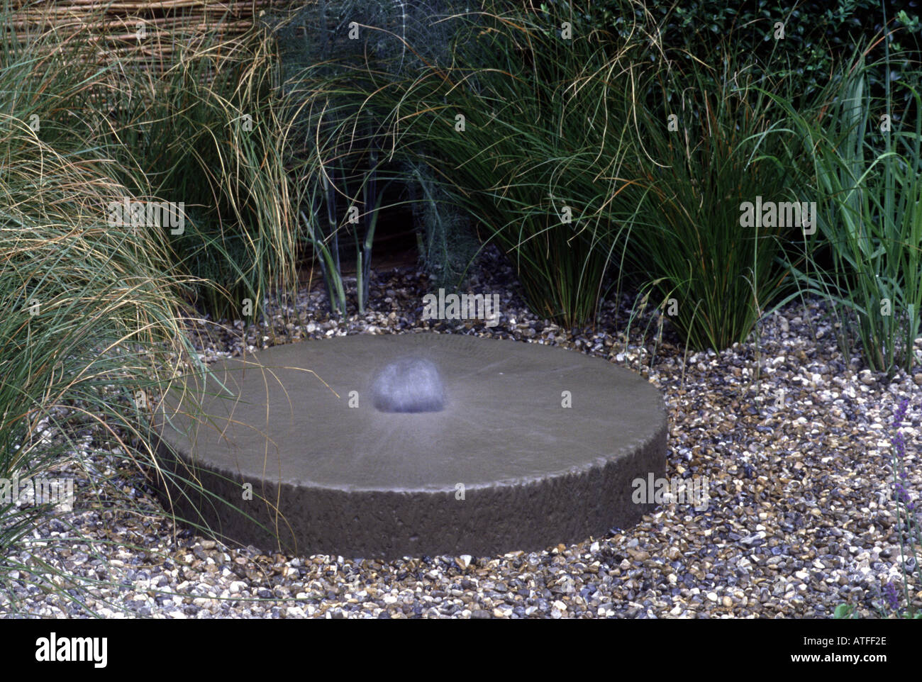 Millstone water feature with ornamental grasses Stock Photo - Alamy