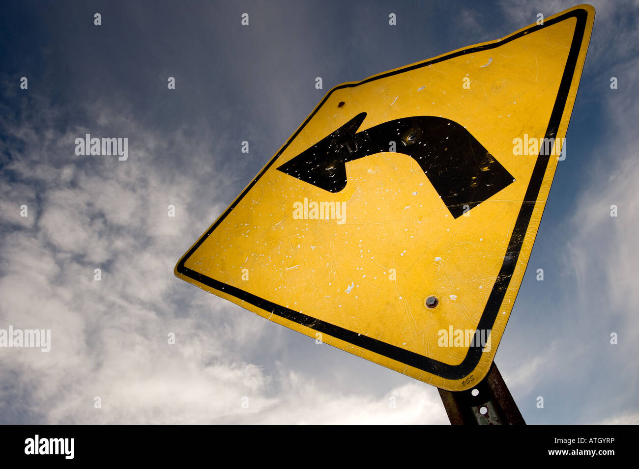 Bright yellow left curve street sign against a cloudy blue sky The sign ...