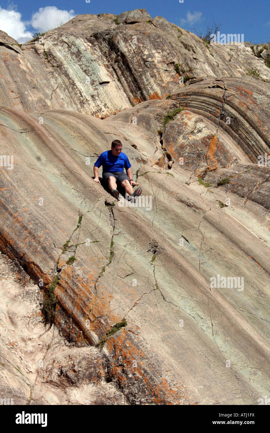 American man sliding down the natural rock slides at the Sacsayhuaman ...