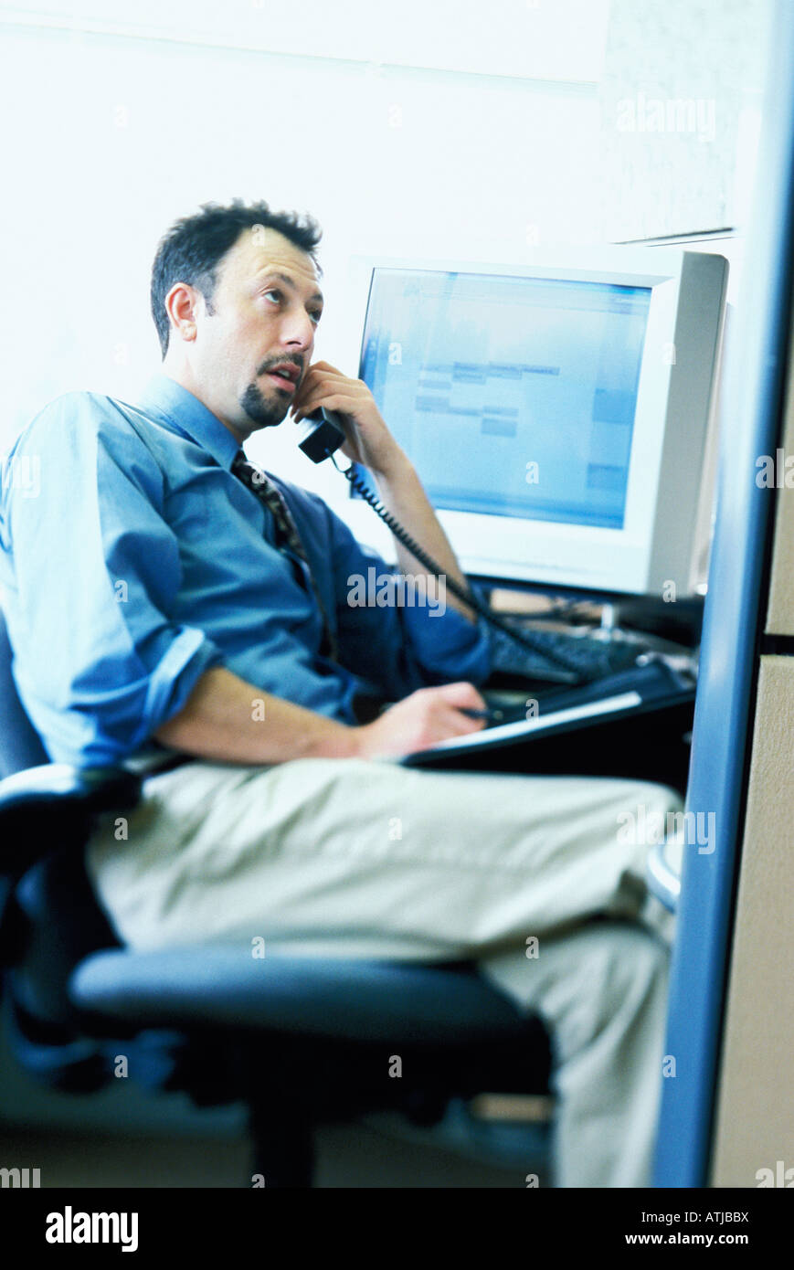 A businessman seated in an office cubicle talking on the telephone ...