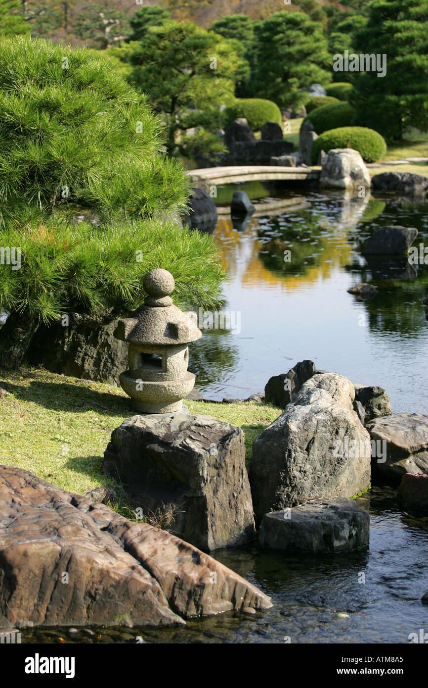An iconic Japanese stone lantern stands next to a stream in a Japanese ...