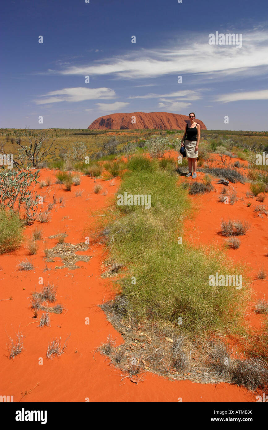 A tourist adds perspective to bright red sand leading up to Ayers rock ...