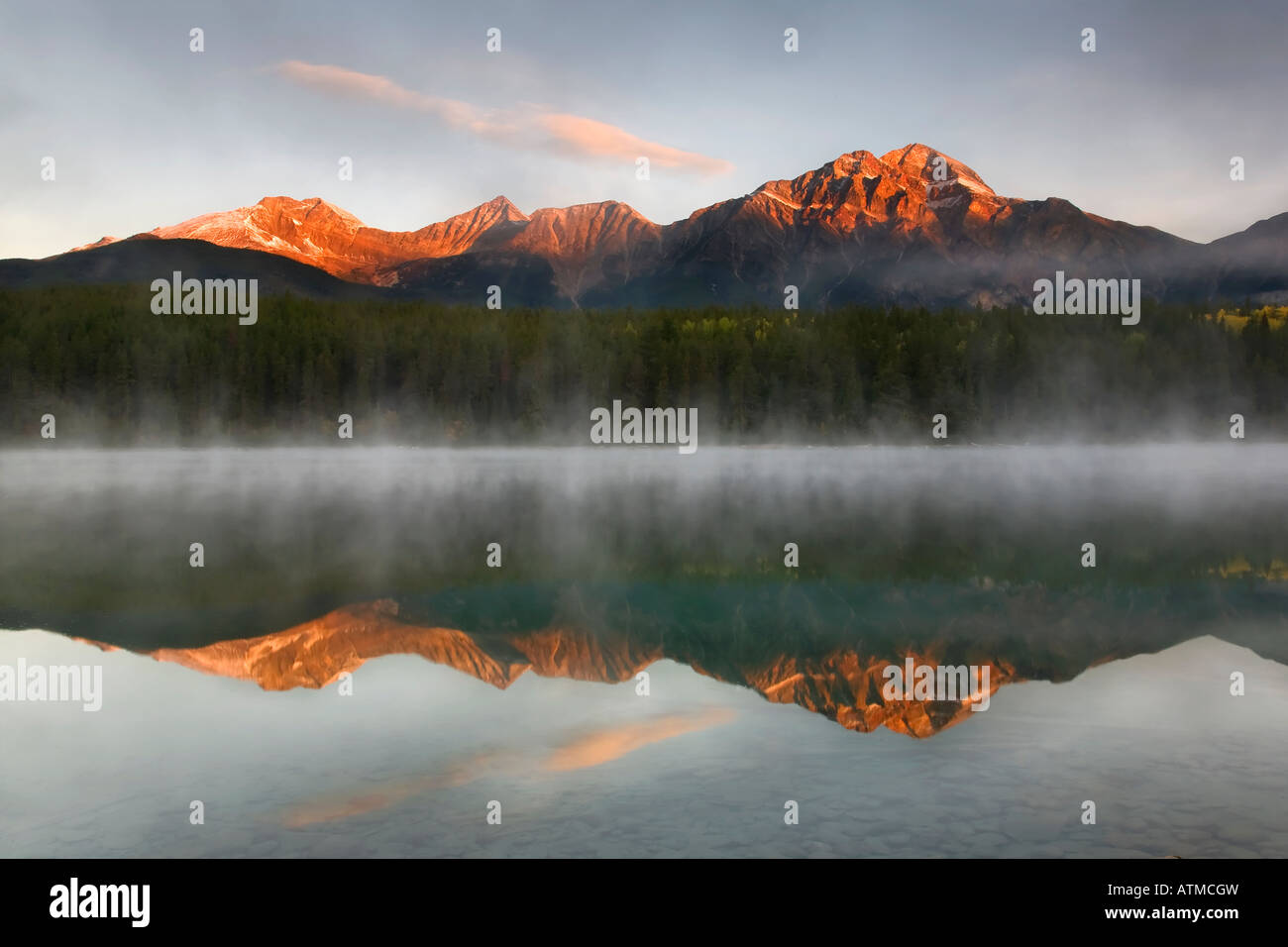A misty morning sunrise over patricia lake with the sunlight lighting ...
