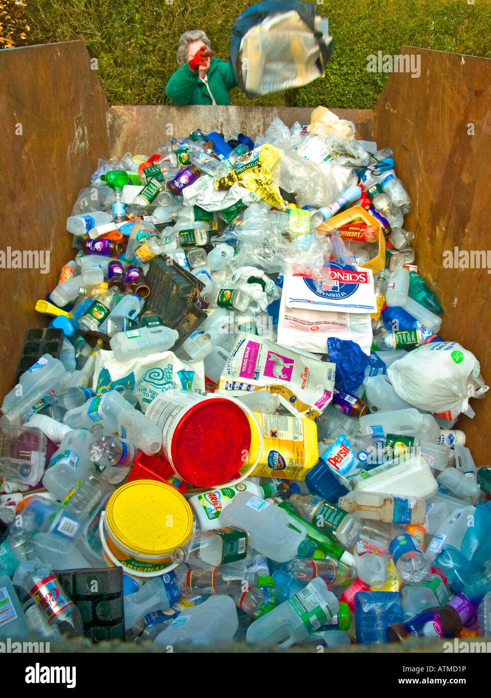 Woman tipping empty plastic containers and wrappers into a special skip ...