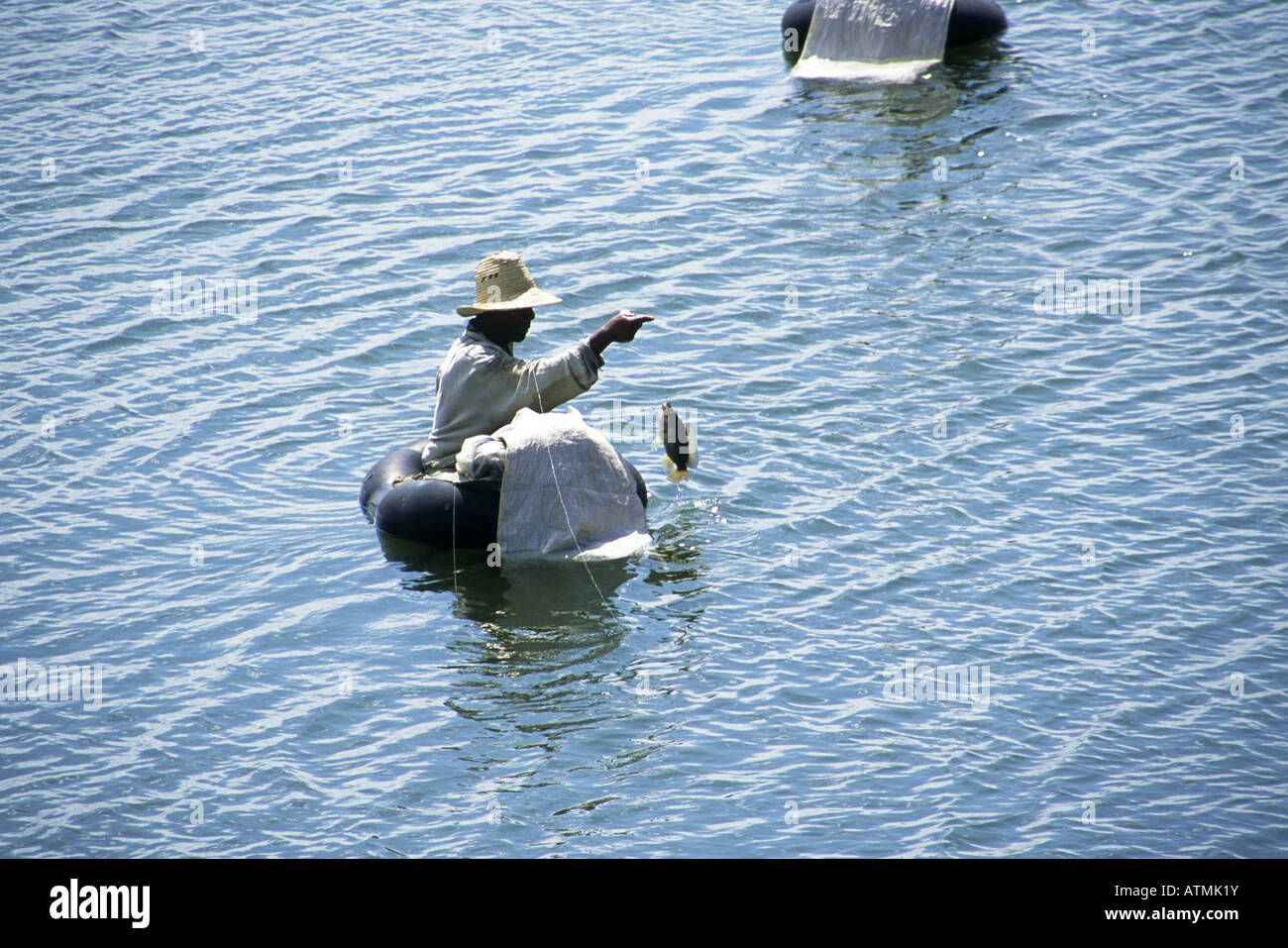 Fishing Man seated in inflated inner tube of car tyre Pulling fish from ...