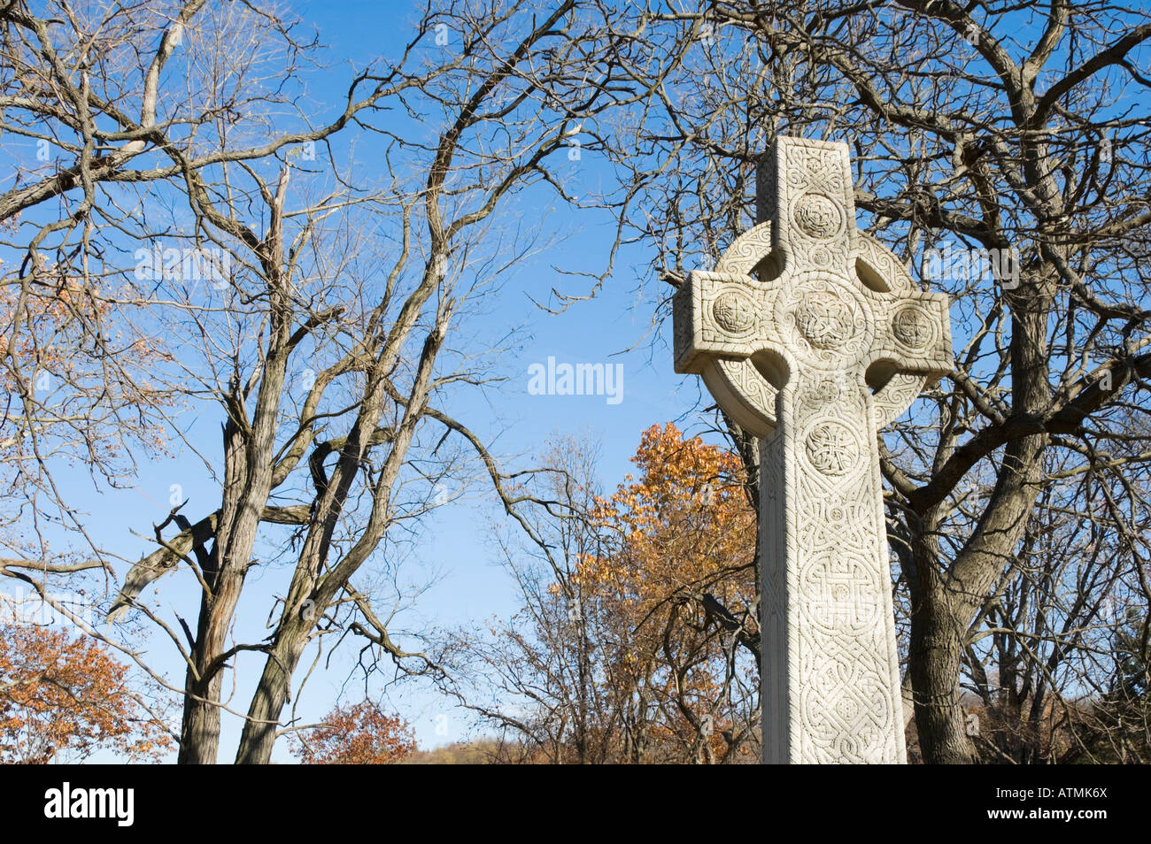 Celtic cross in granite with bare trees and limbs in a fall cemetery ...
