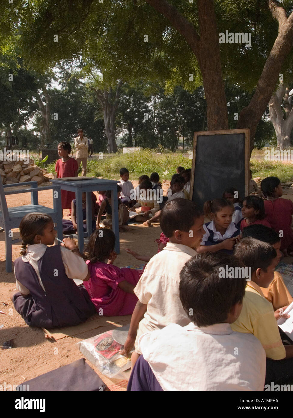 Well behaved junior school children sat on ground outside rural village ...