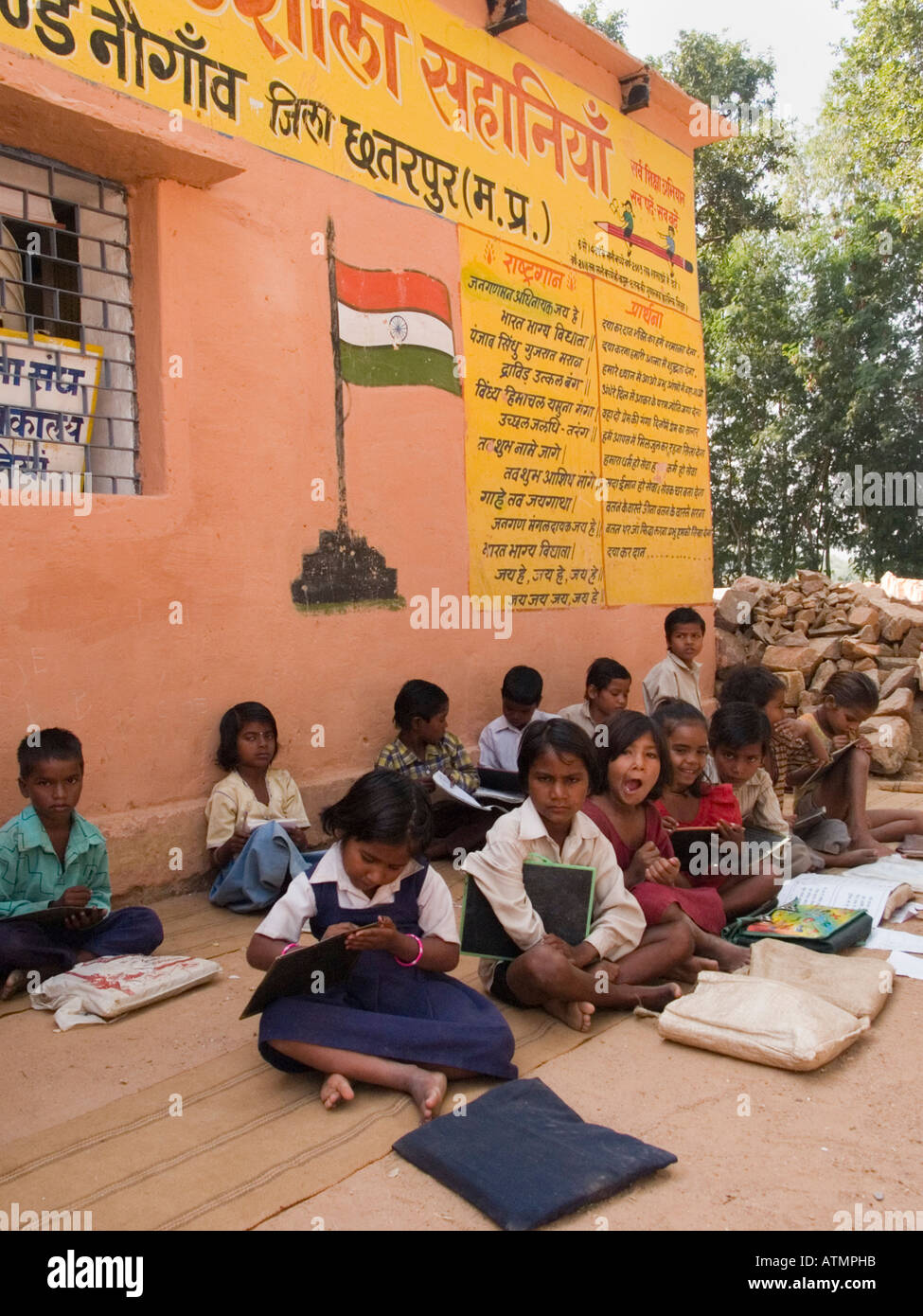 Rows of well behaved junior school children sat on ground in shade ...