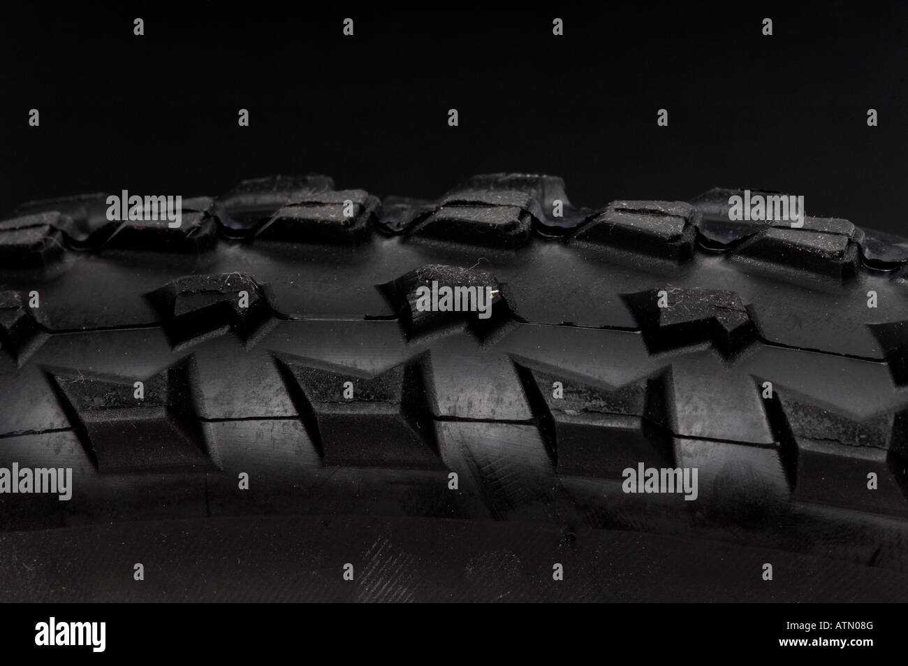 Closeup of the tread on a black mountain bike tyre seen against a black ...