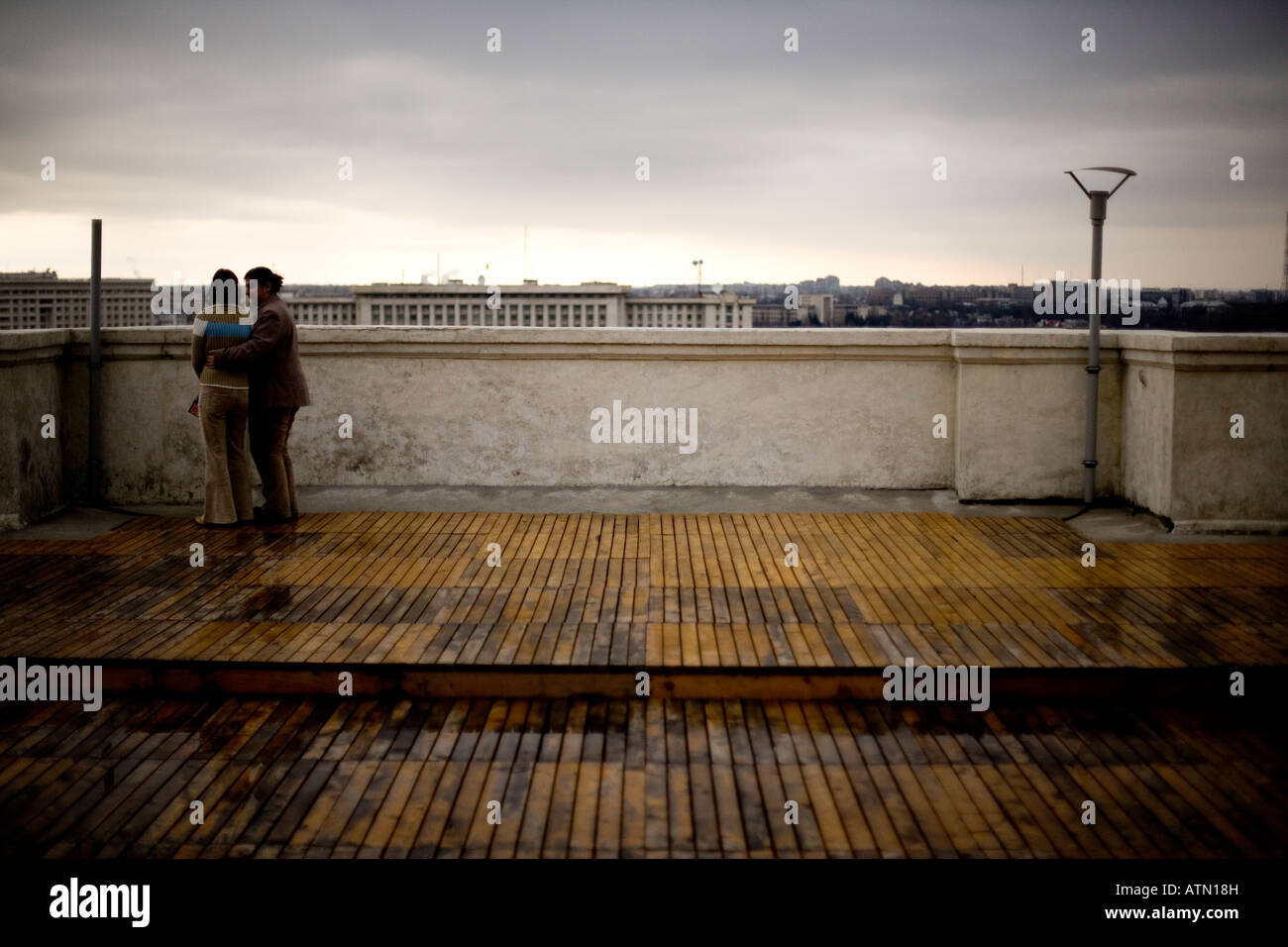 a man and a woman hugging on the roof of a building looking at the ...