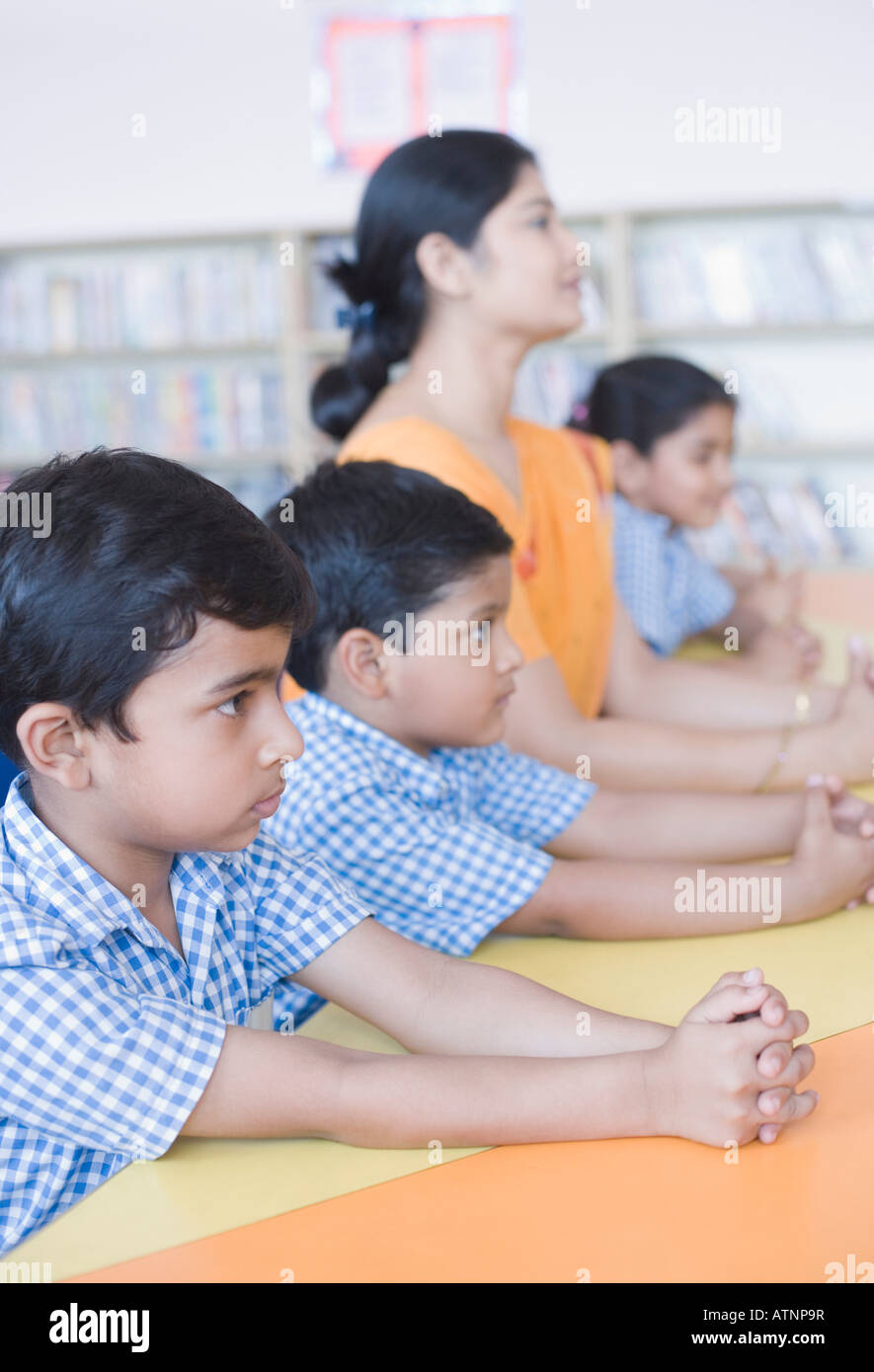 Side profile of a female teacher sitting at a desk with her students in ...