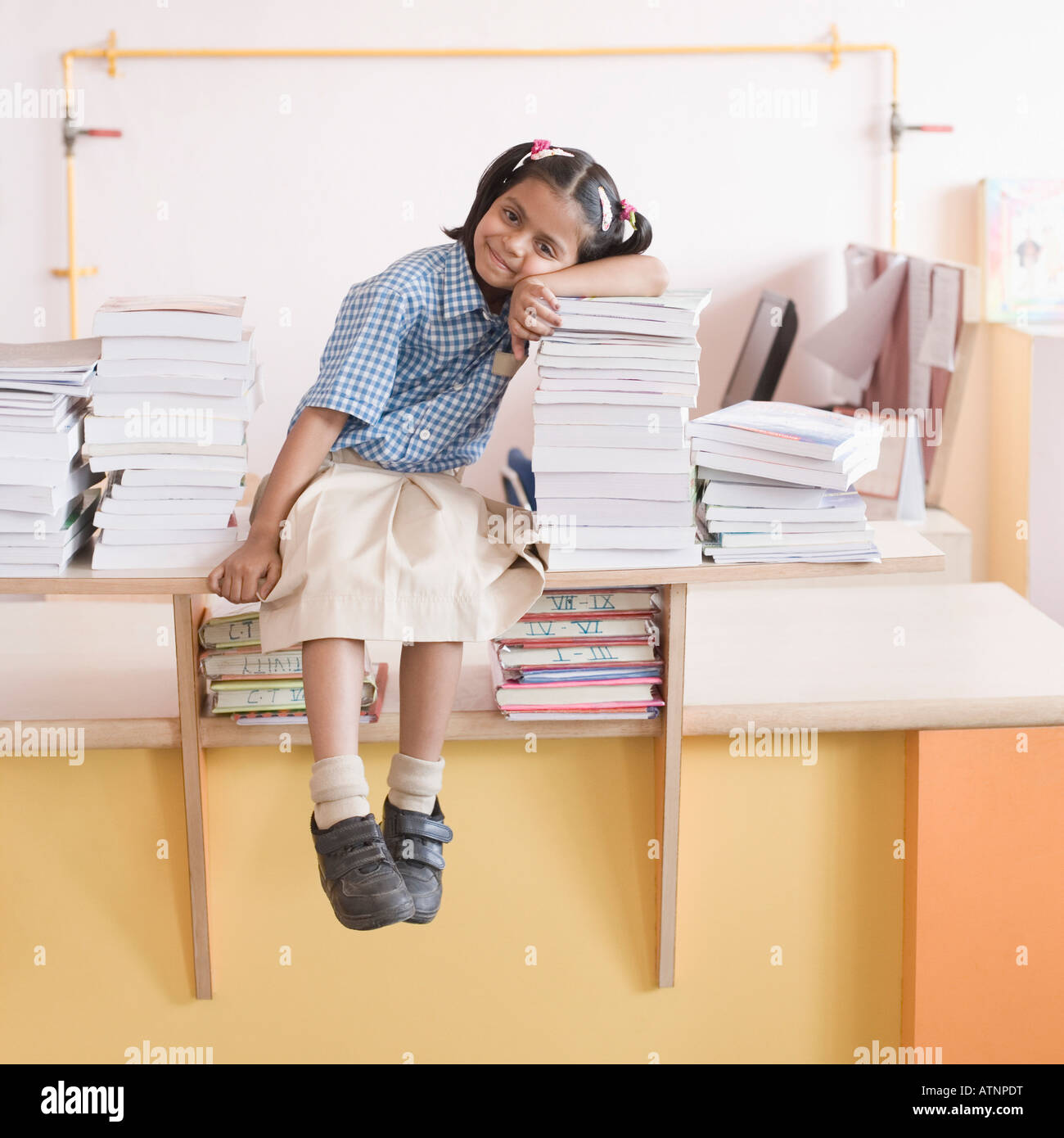 Schoolgirl sitting on a shelf and leaning against a stack of books ...