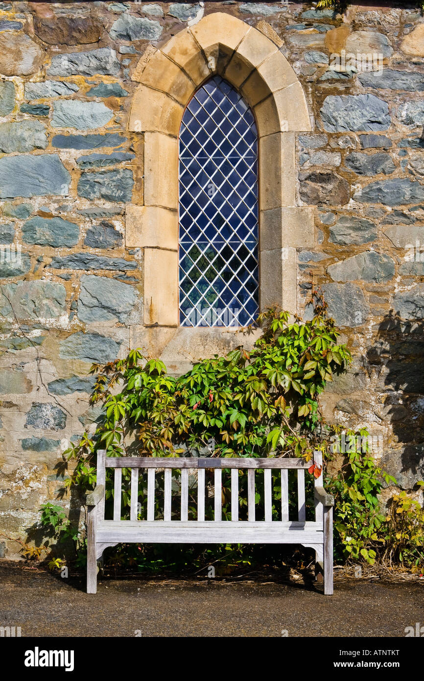 White bench below an antique window with ivy climbing the old chapel ...