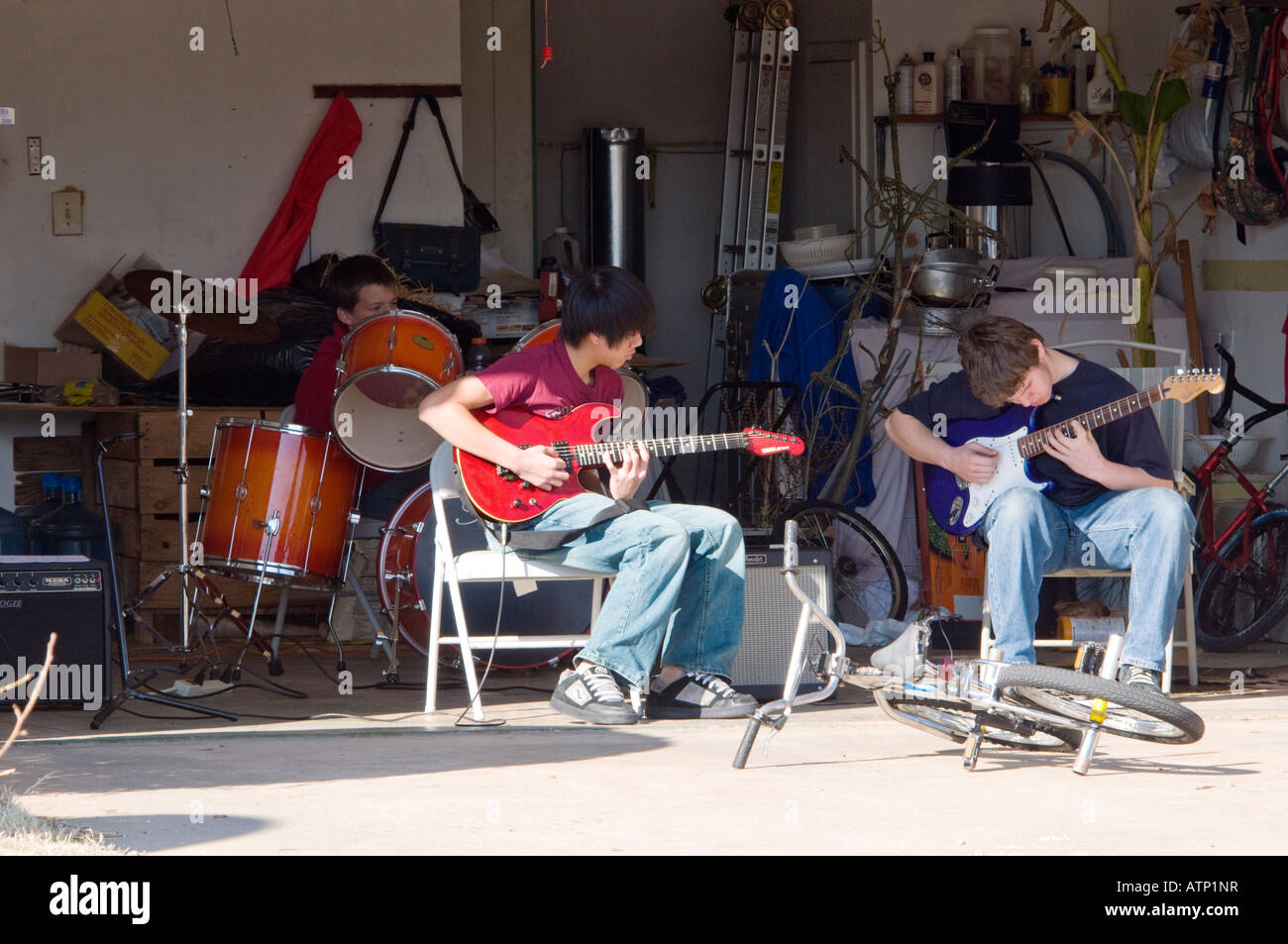Three teenage boys who have formed a garage band, practice music in a ...