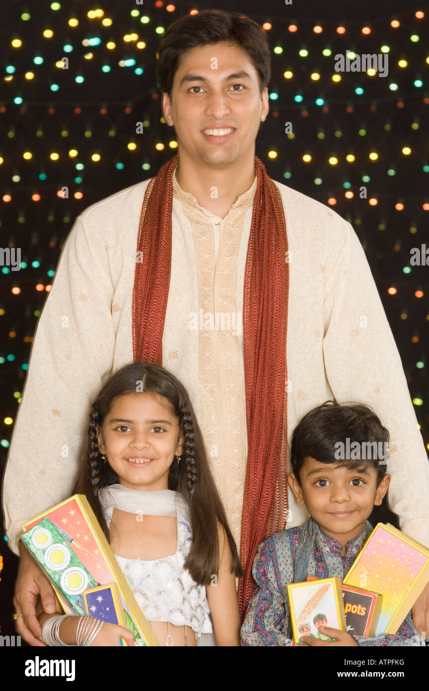 Portrait of a young man standing with his son and daughter and holding ...