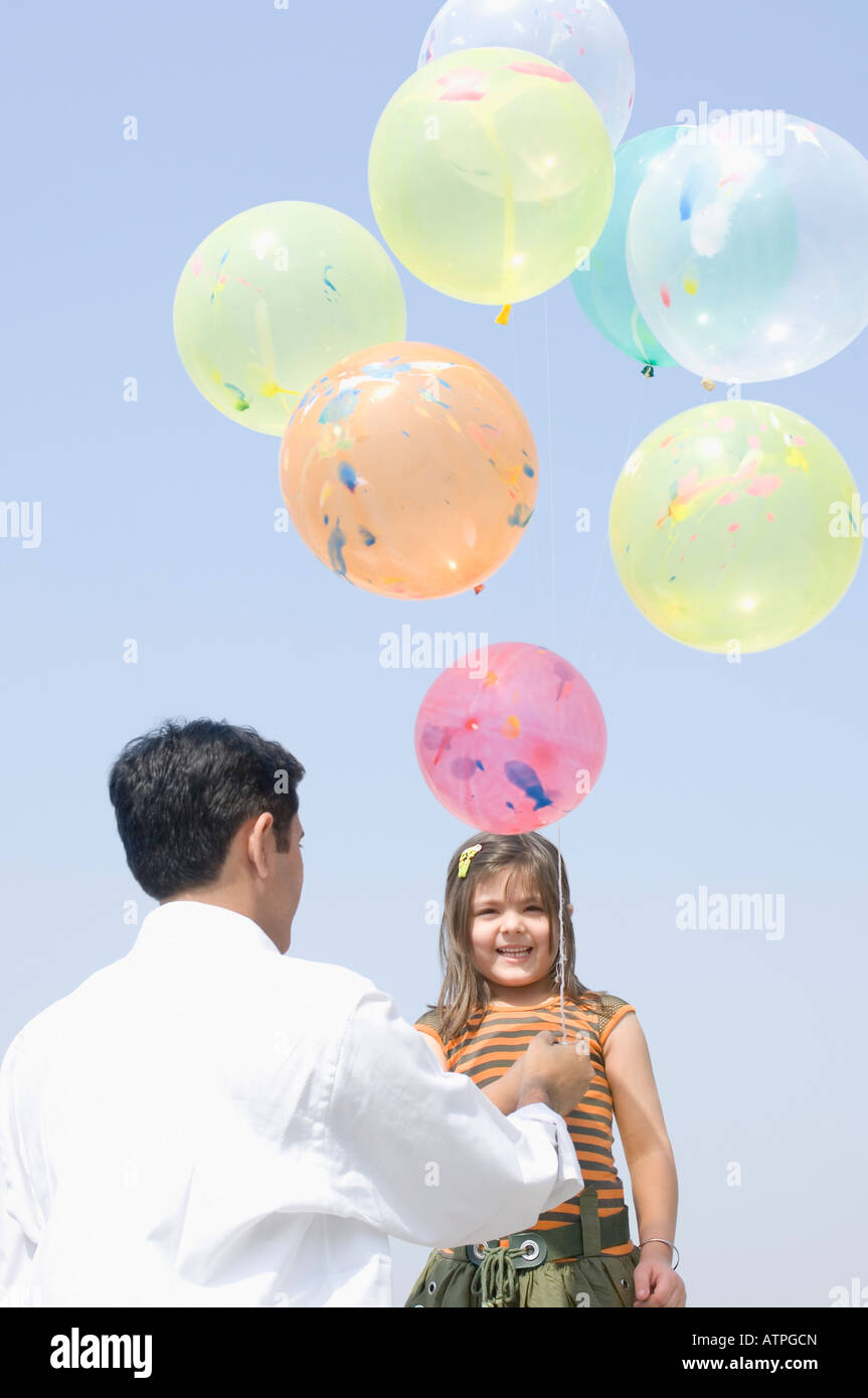 Rear view of a mid adult man giving balloons to his daughter Stock ...