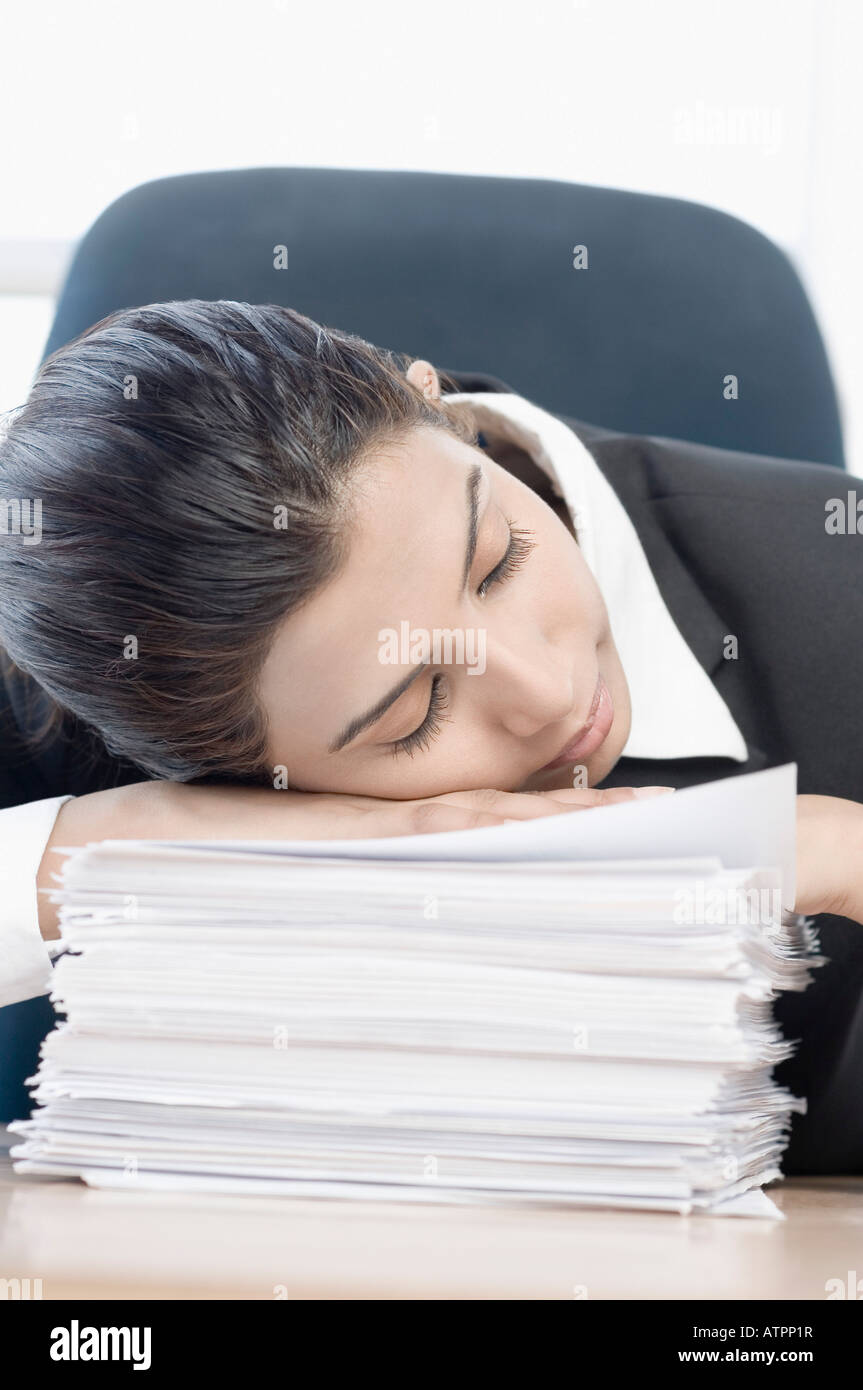 Close-up of a businesswoman leaning on a stack of papers and sleeping ...