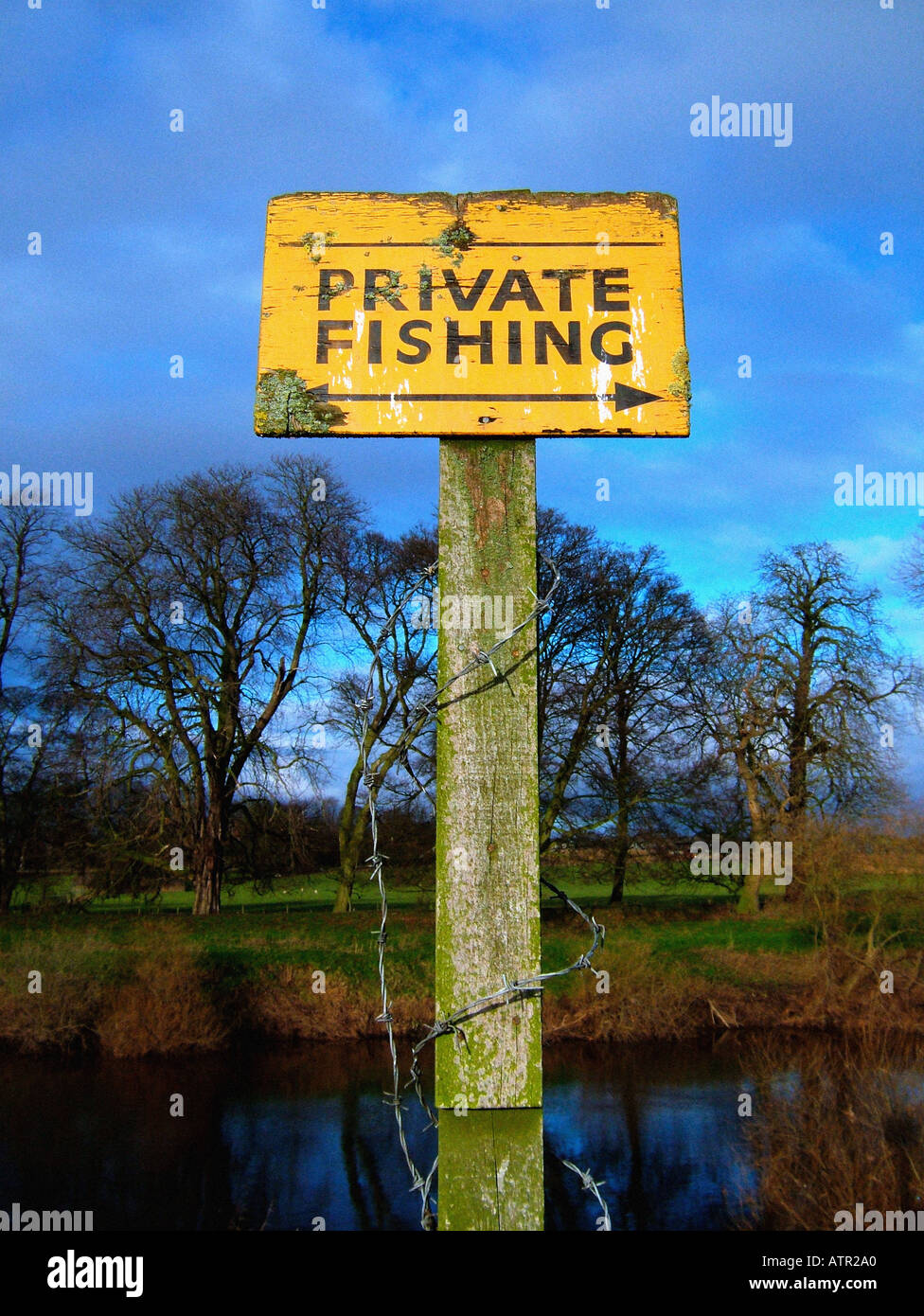 Yellow Private Fishing sign at side of river with trees in background ...