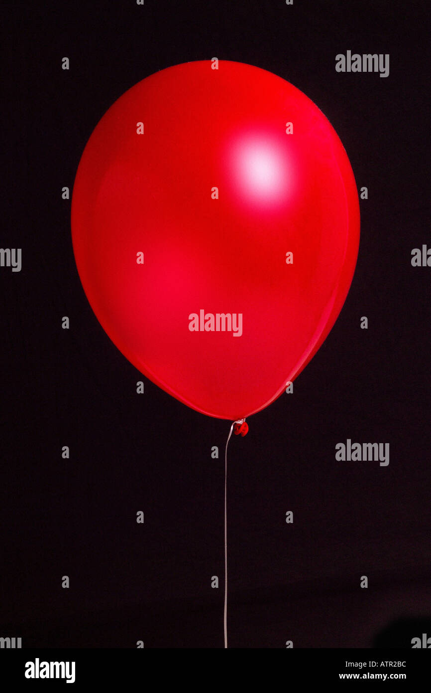 Single red helium balloon on white ribbon against black background ...