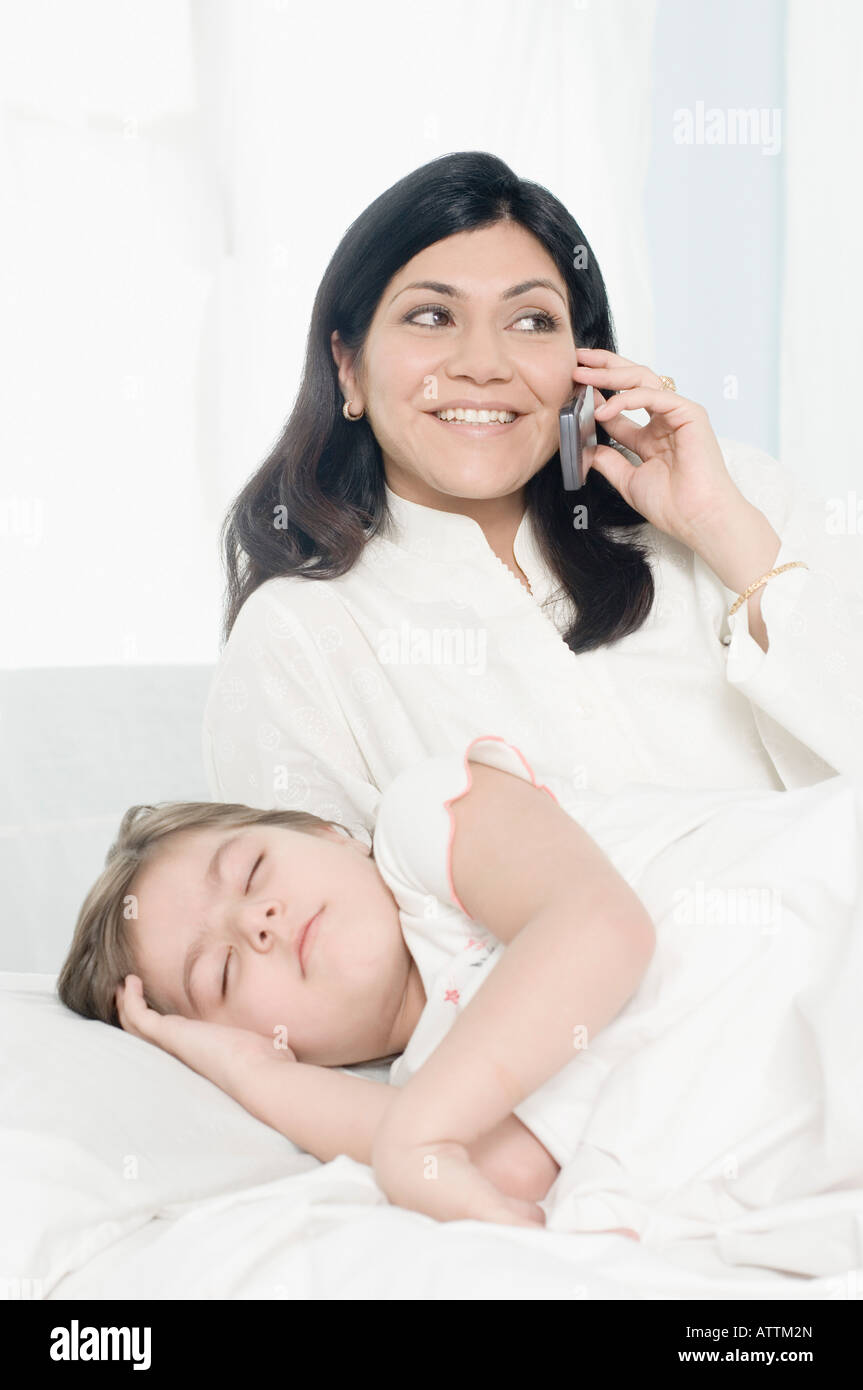Mid adult woman talking on a mobile phone with her daughter sleeping ...