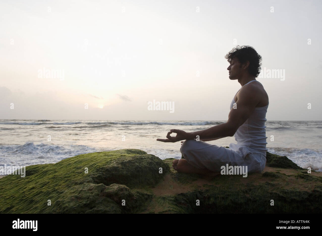 Side profile of a young man meditating in lotus position on the beach ...