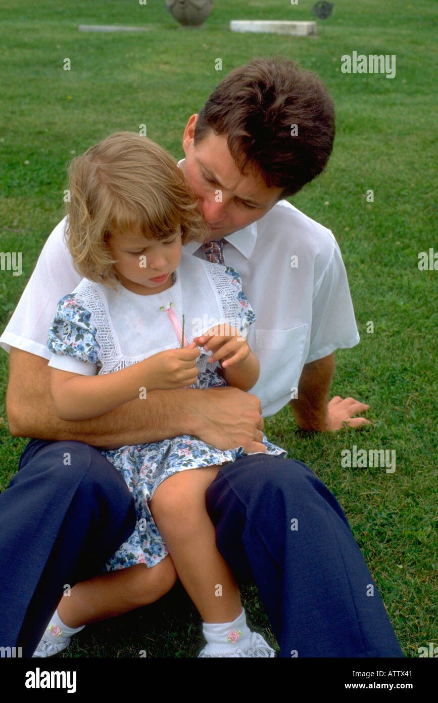 Father age 35 embracing and comforting daughter age 5 at funeral grave ...