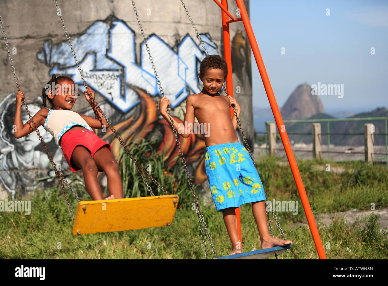 Children play on swing in Rio de Janeiro favela slum with graffiti ...