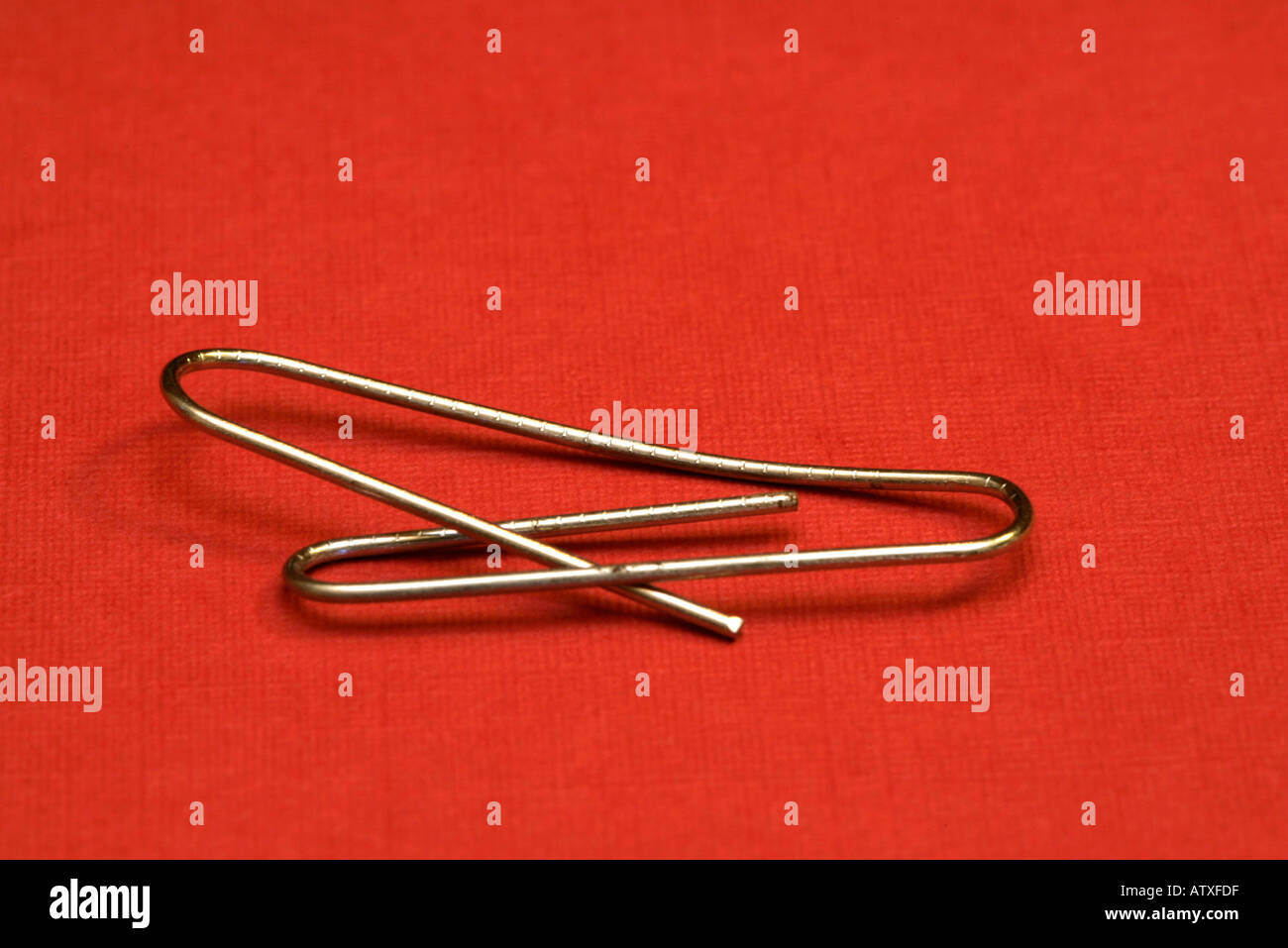 Bent paper clip on red background Stock Photo - Alamy