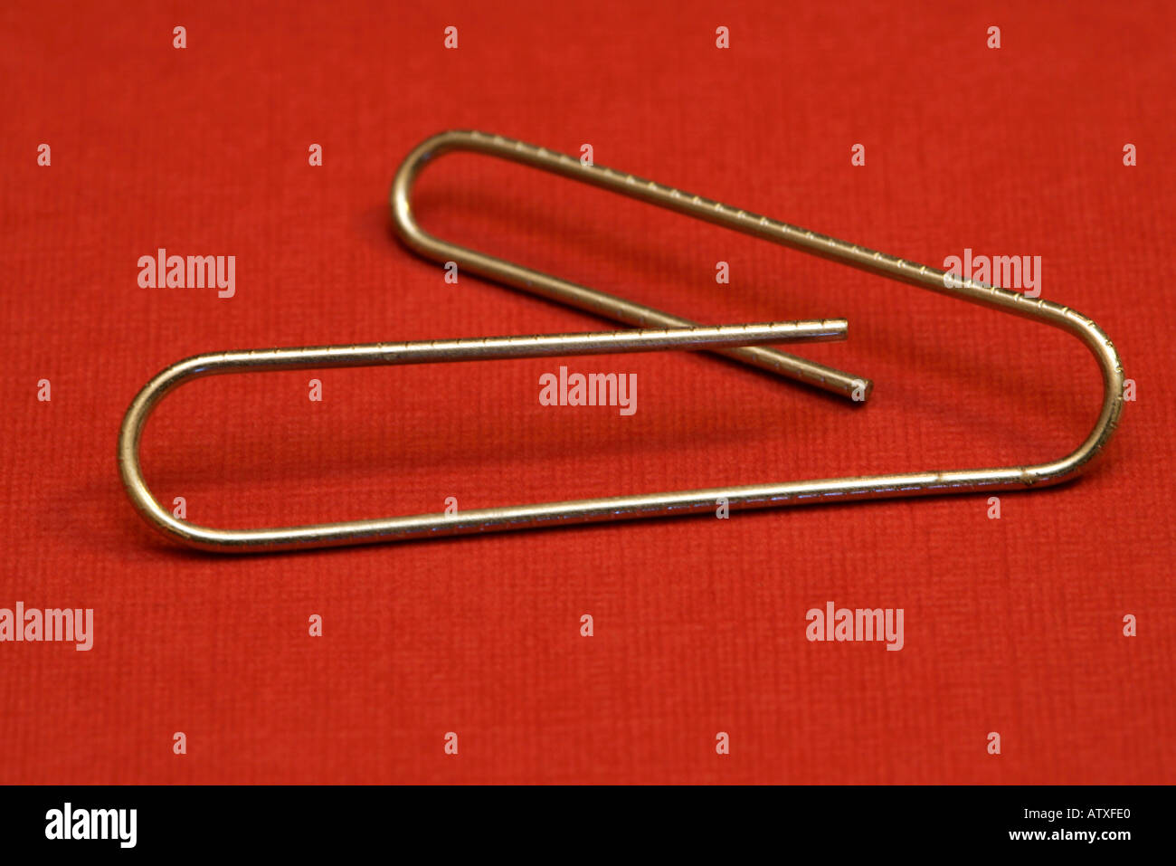 Bent paper clip on red background Stock Photo - Alamy