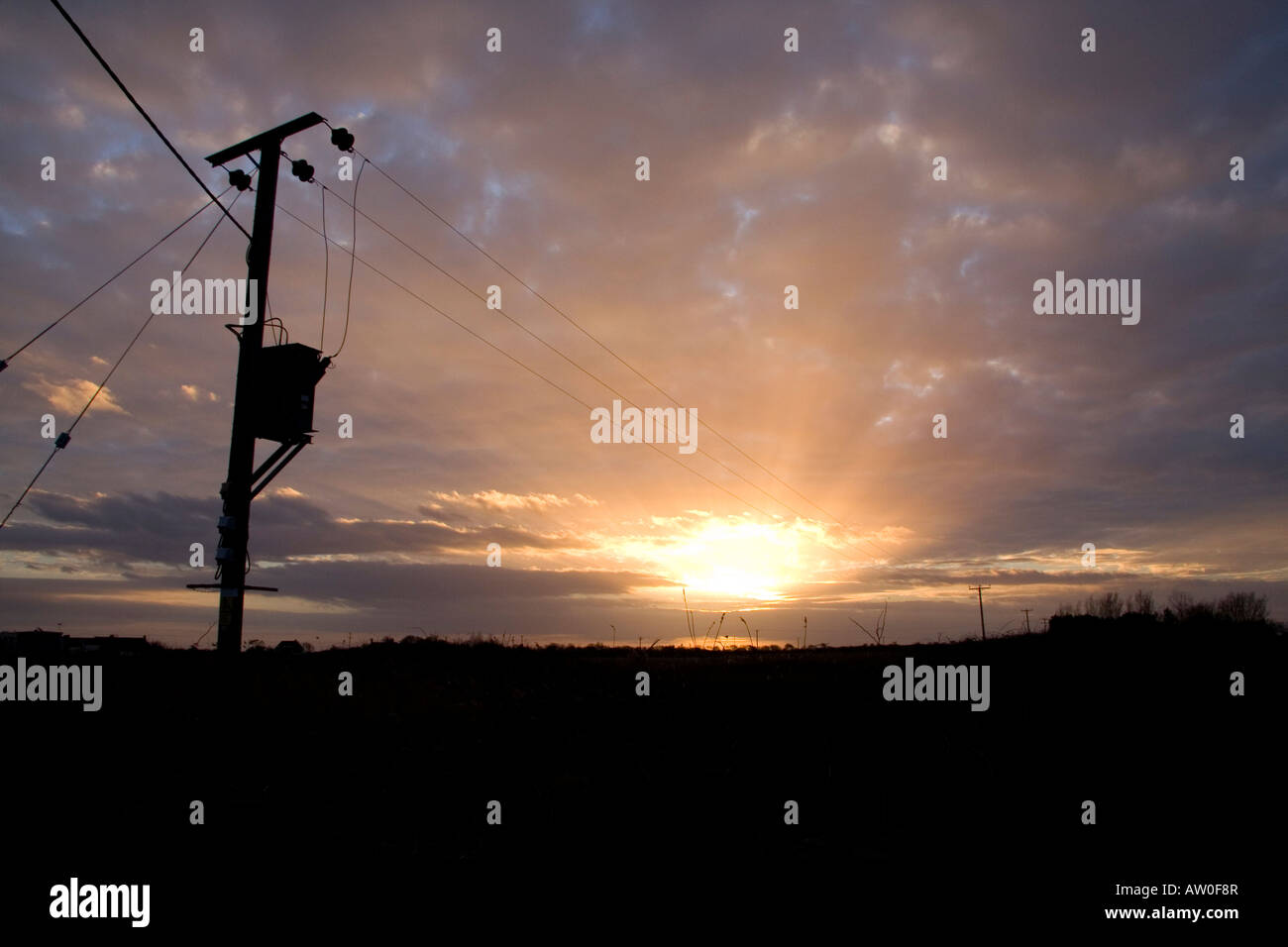 Electricity pole transformer and wires silhouetted against sunset ...