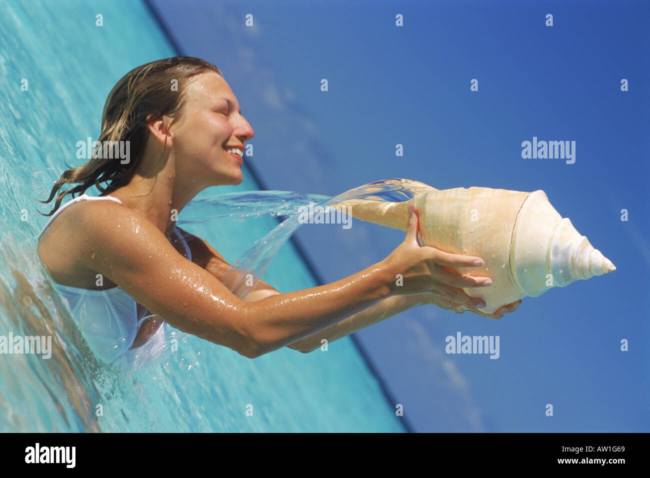 Woman chilling out using giant conch shell to pour ocean water over her face and body Stock ...