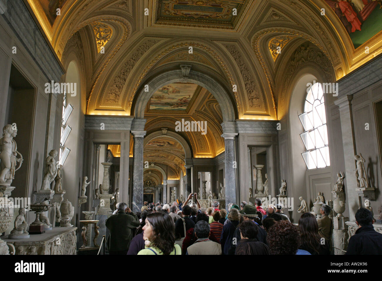 Tourists admire the statues and sculptures in a bright corridor with ...
