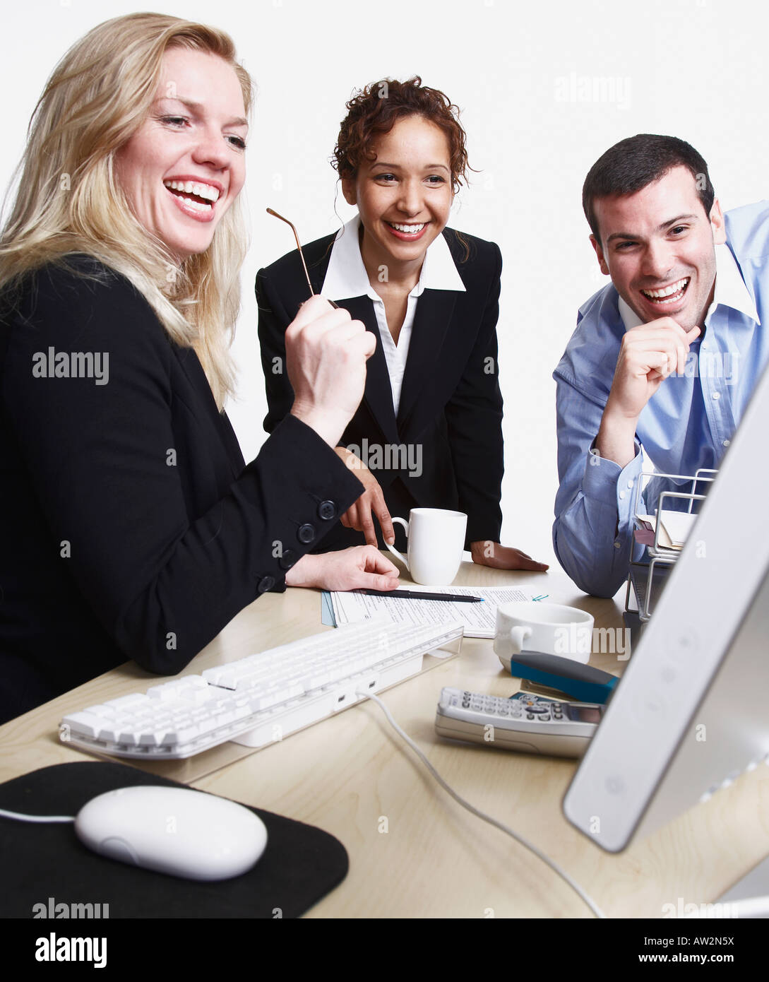 three business people at a desk, looking at computer monitor, smiling ...