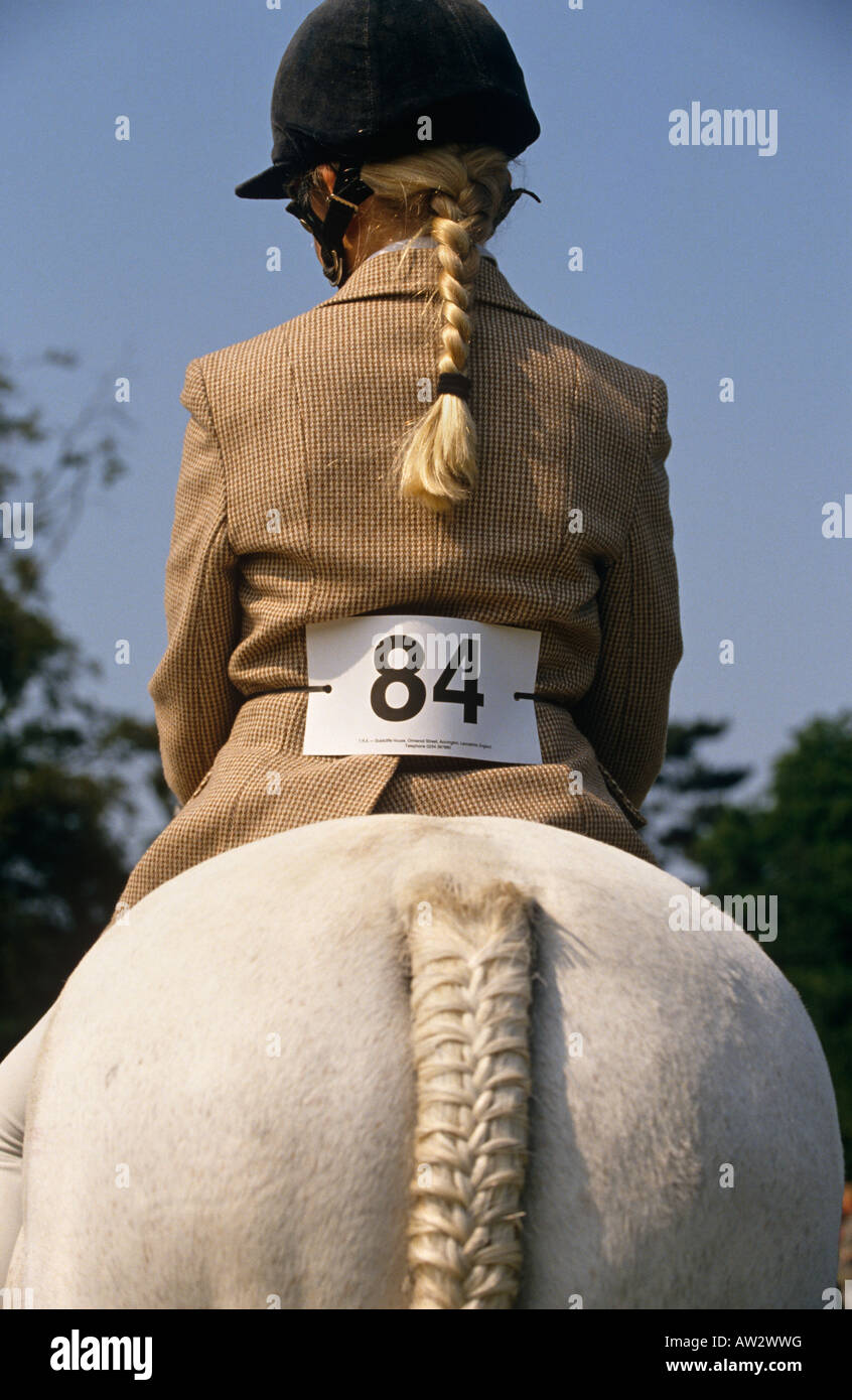 A young rider with a plaited pony tail sits on her horse sporting its ...