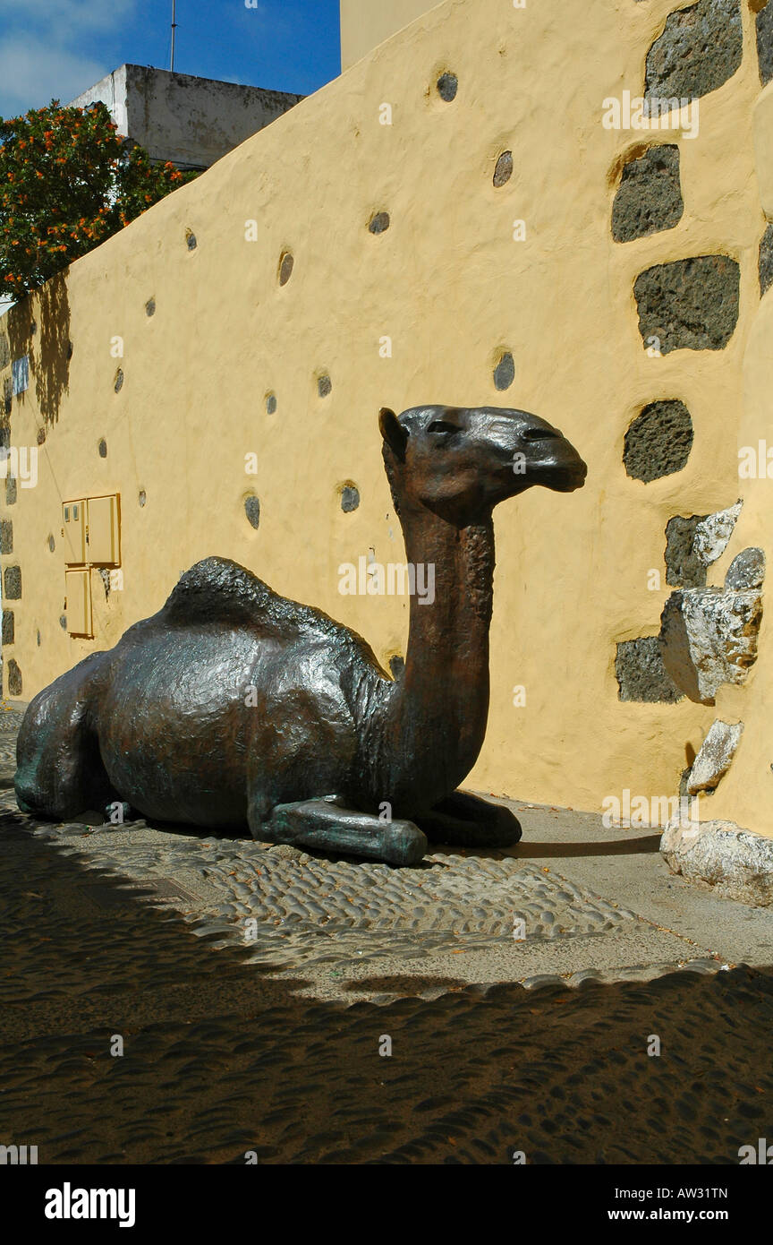 A bronze sculpture of a camel displayed next to typical basalt house in ...